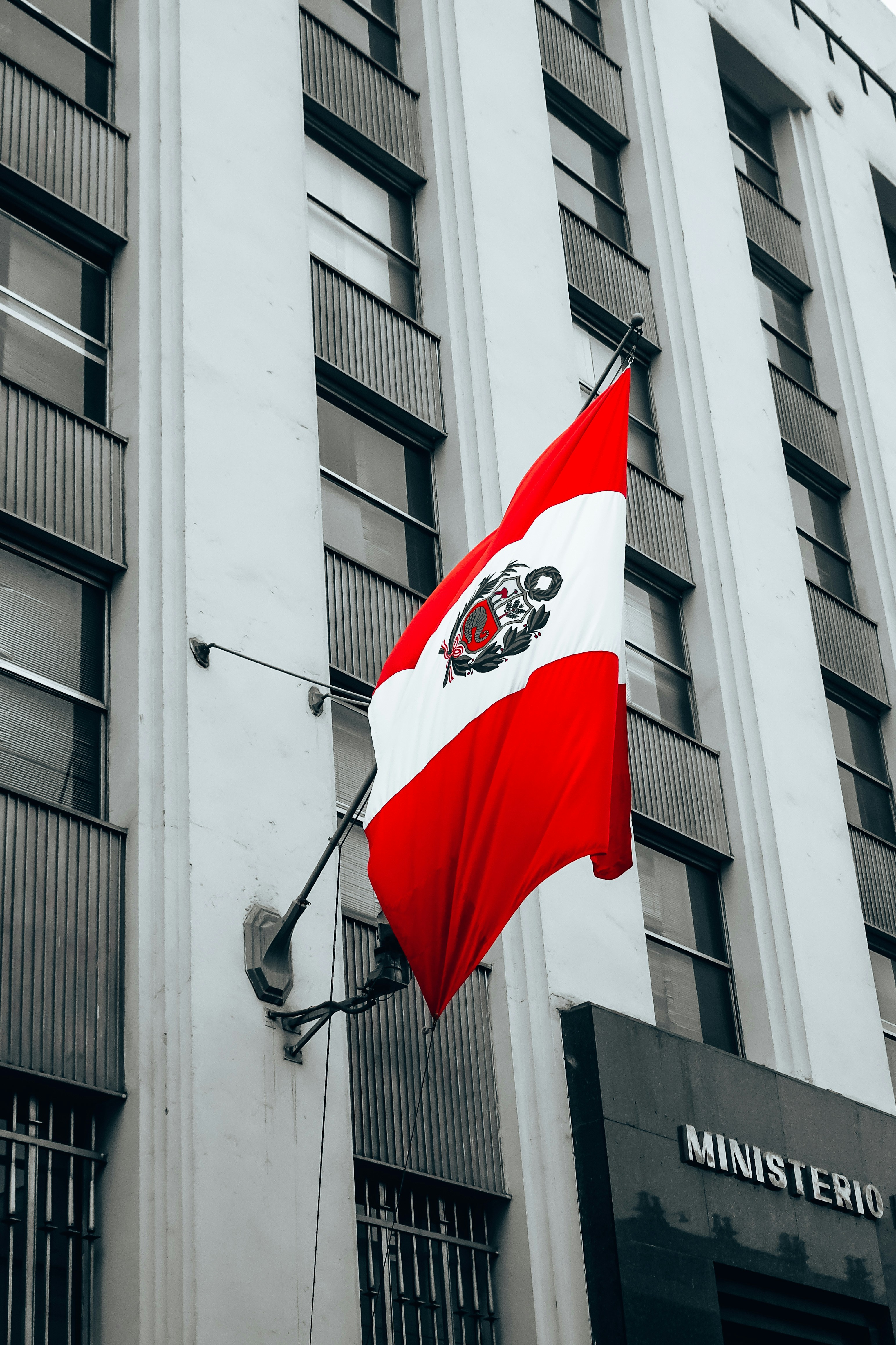 Peruvian flag waving against the backdrop of a white multi-story building facade.
