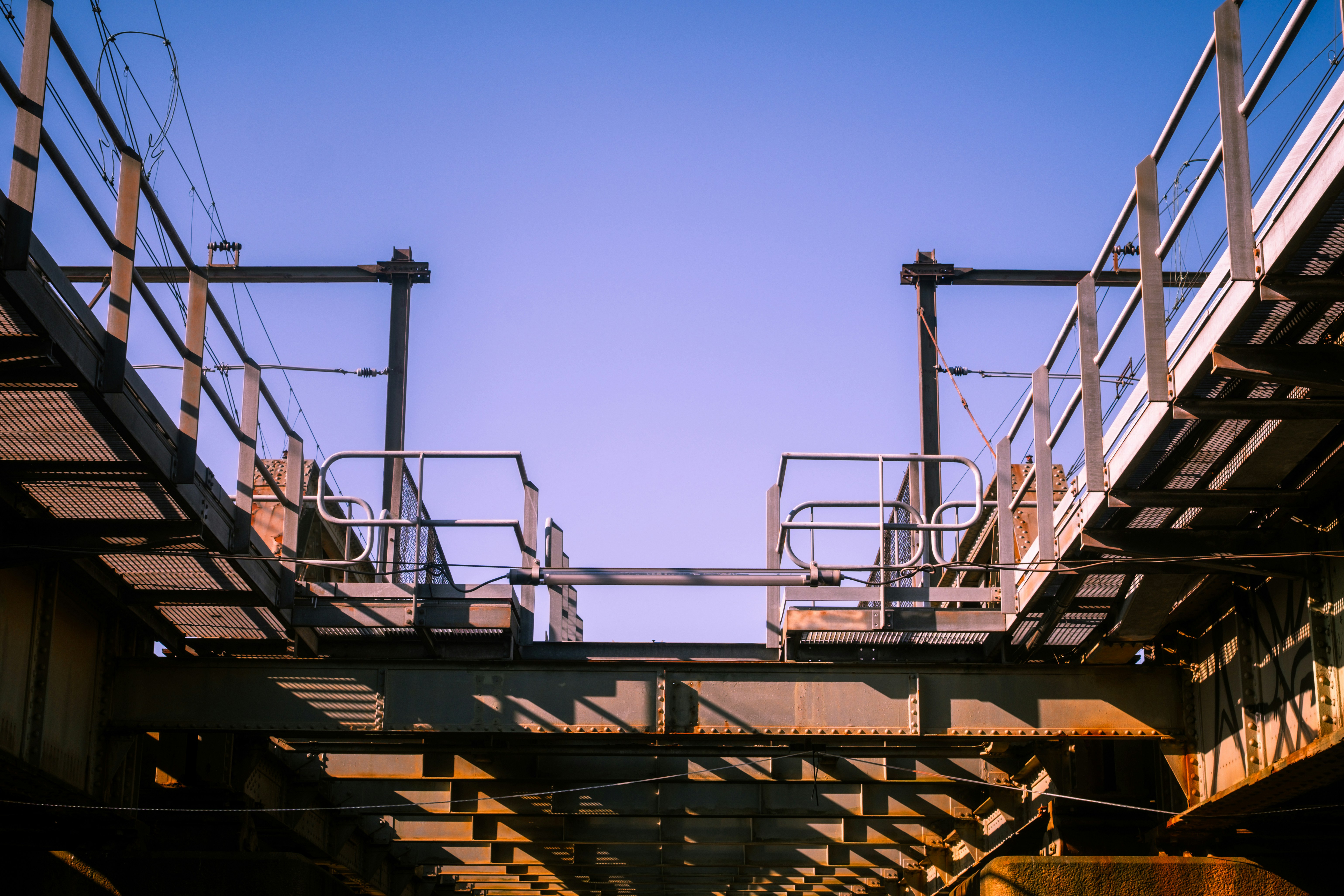 Industrial bridges stretching into a clear blue sky with intricate metalwork and shadow play.