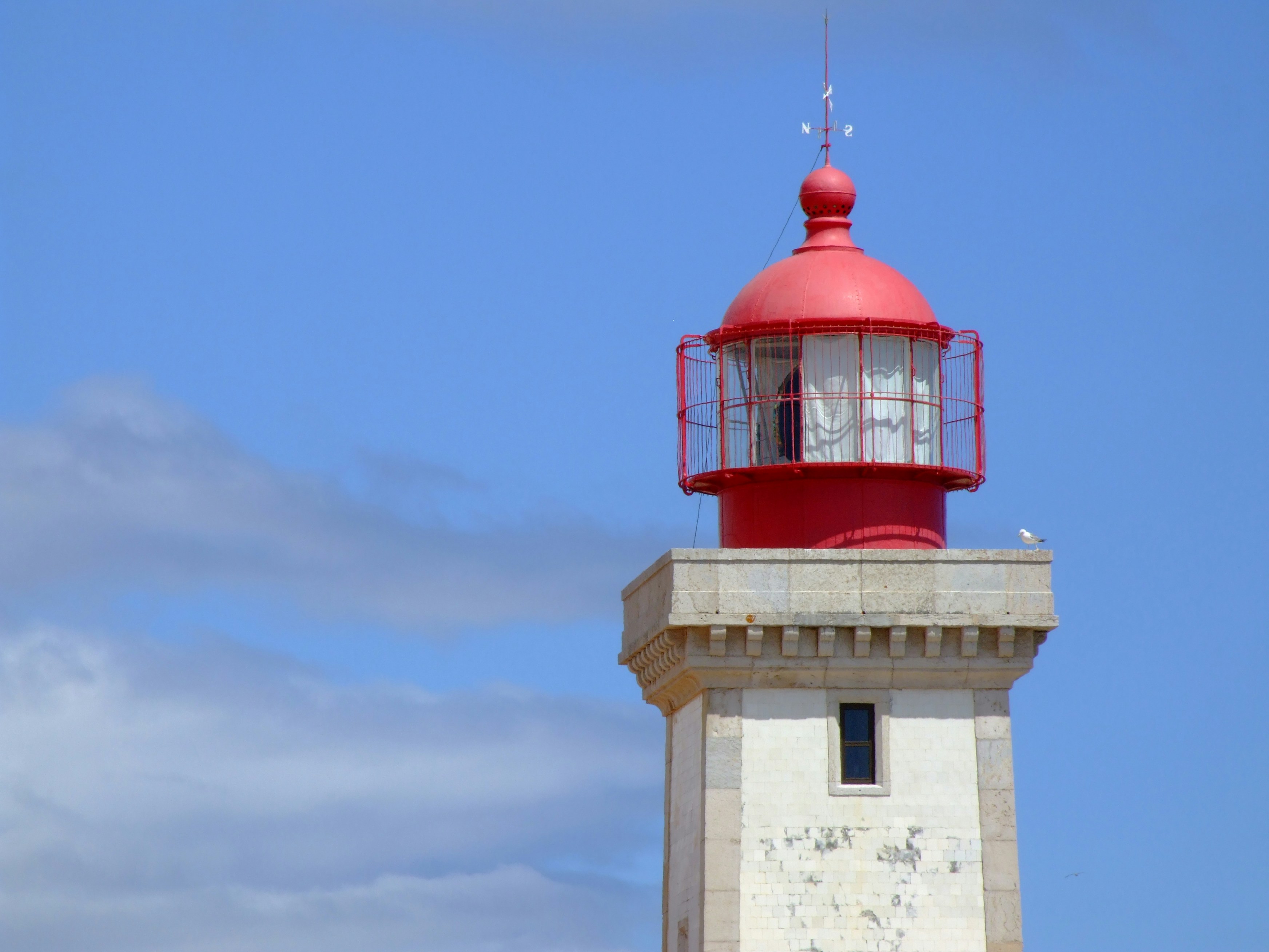 Red lighthouse towering under a vibrant blue sky with scattered clouds.