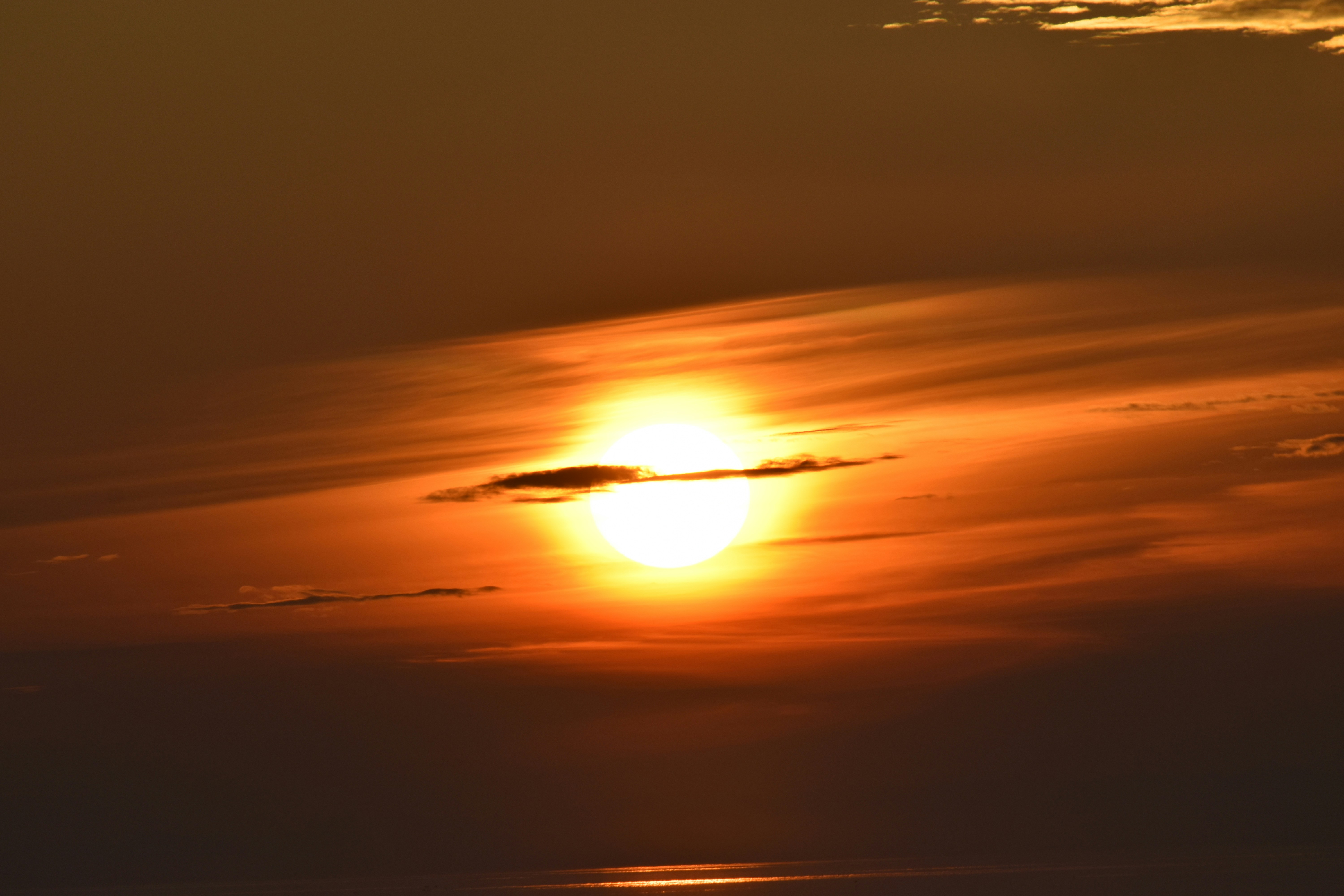 Vibrant sun setting behind streaks of orange clouds over a darkened horizon.