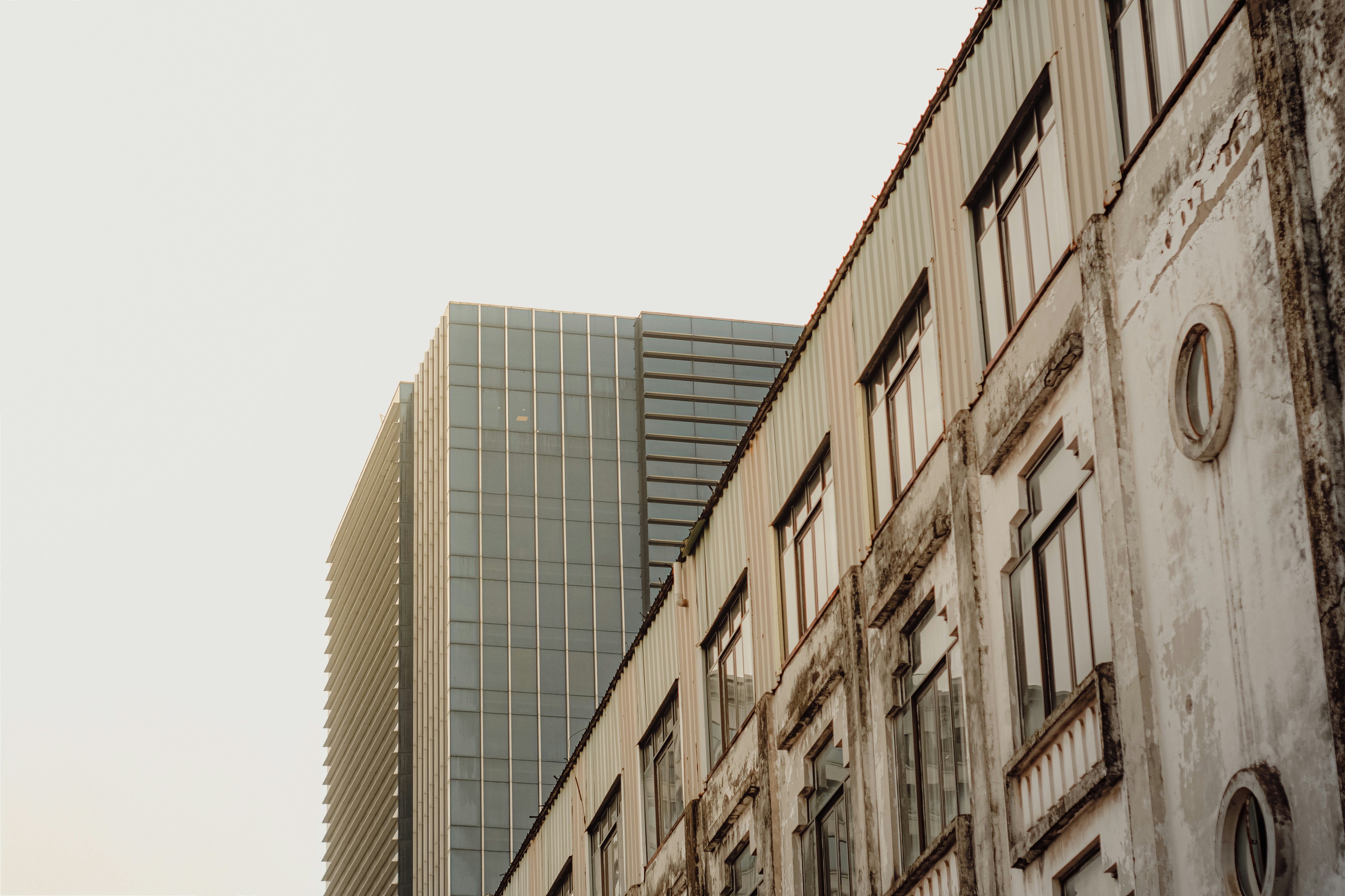Juxtaposition of modern glass skyscraper and weathered historic building under soft light.