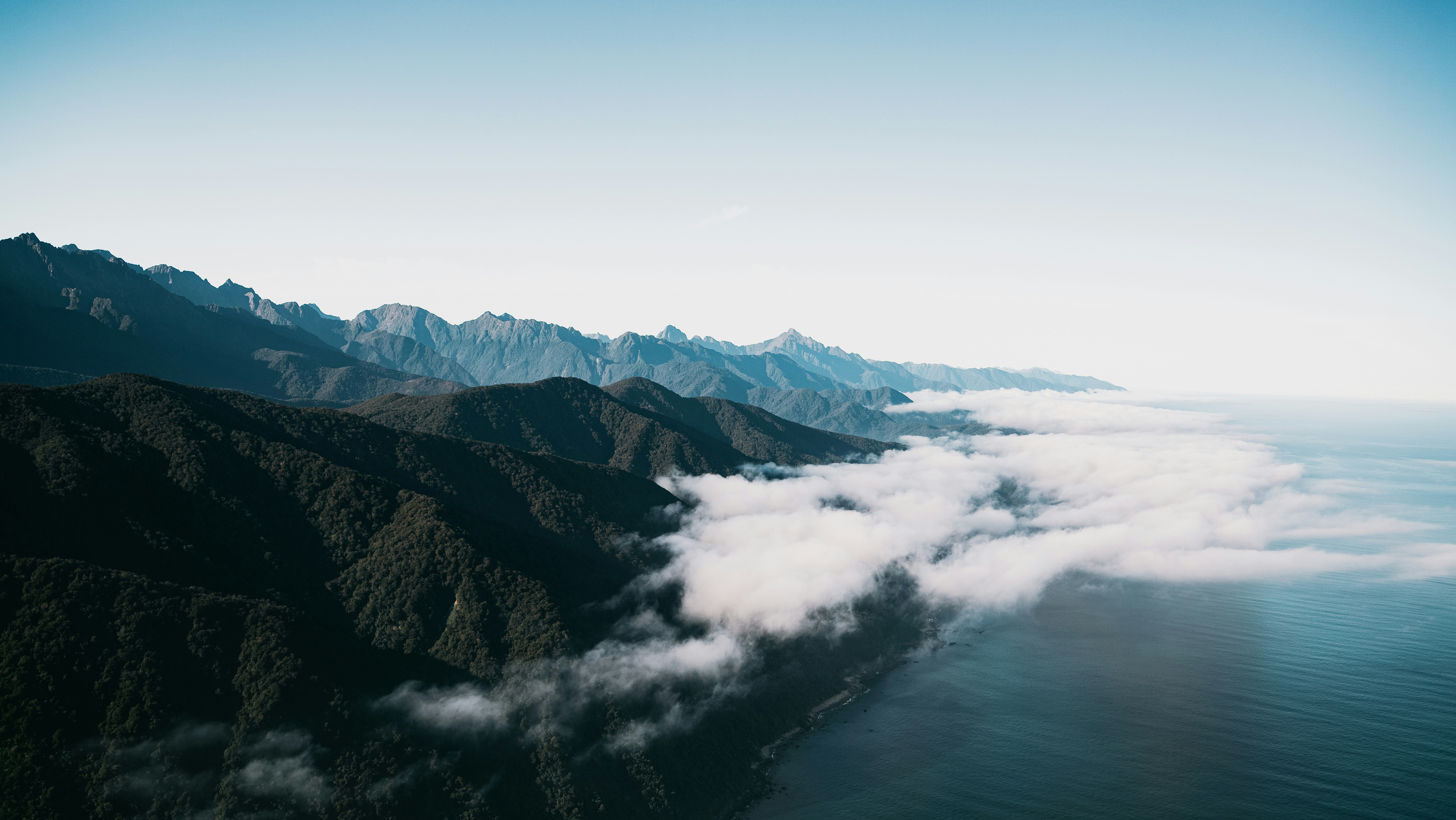 Mountains meet the sea amidst clouds and mist. photo – Free Full hd wallpaper Image on Unsplash