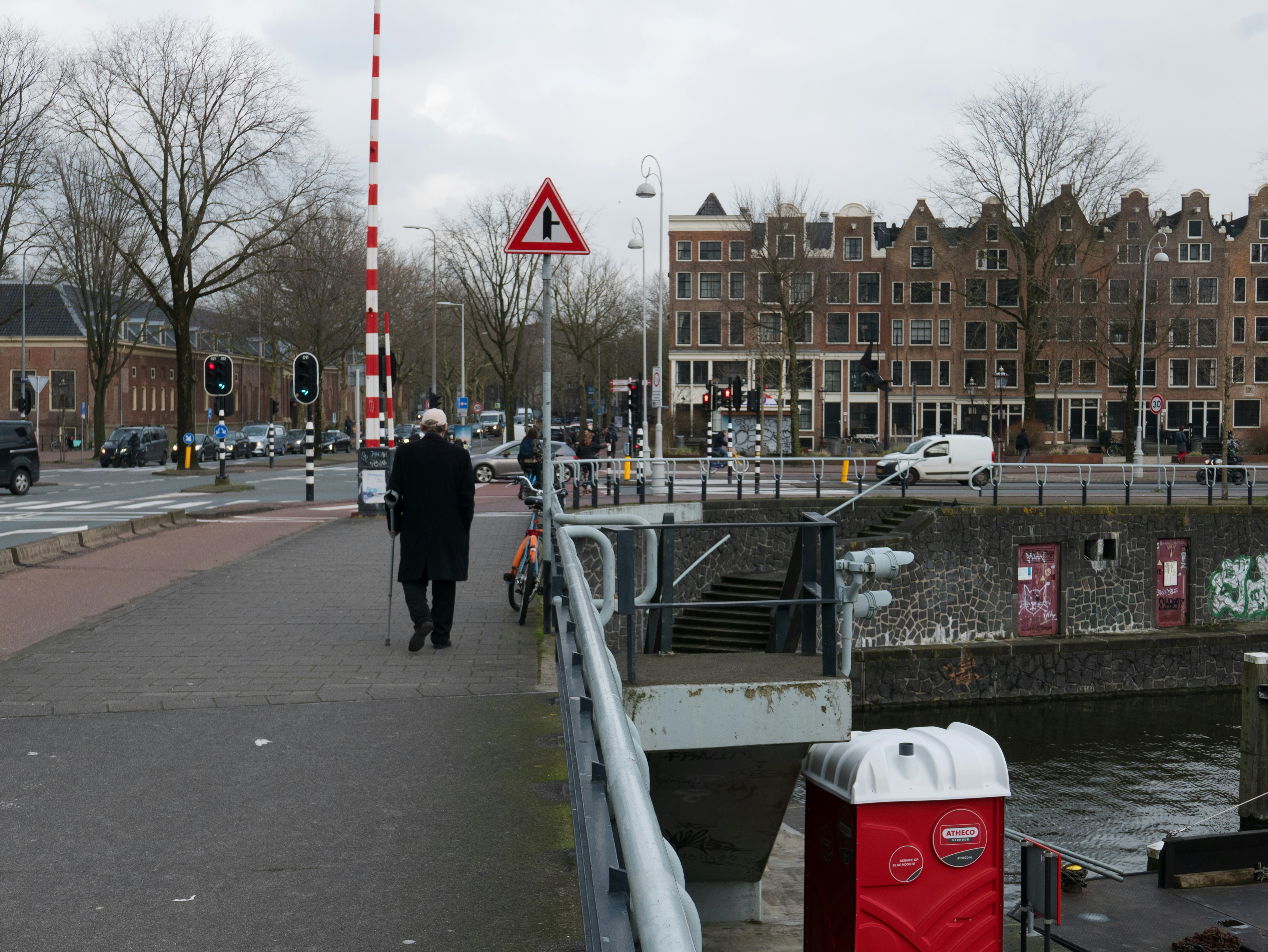 Free photo of a man walking over the bridge Kattenburgerbrug in Amsterdam city. It is winter in town with bare trees and a grey sky. Street photography of The Netherlands in free download images // Foto van man, wandelend over de Kattenburgerbrug in Amsterdam, gratis download foto.