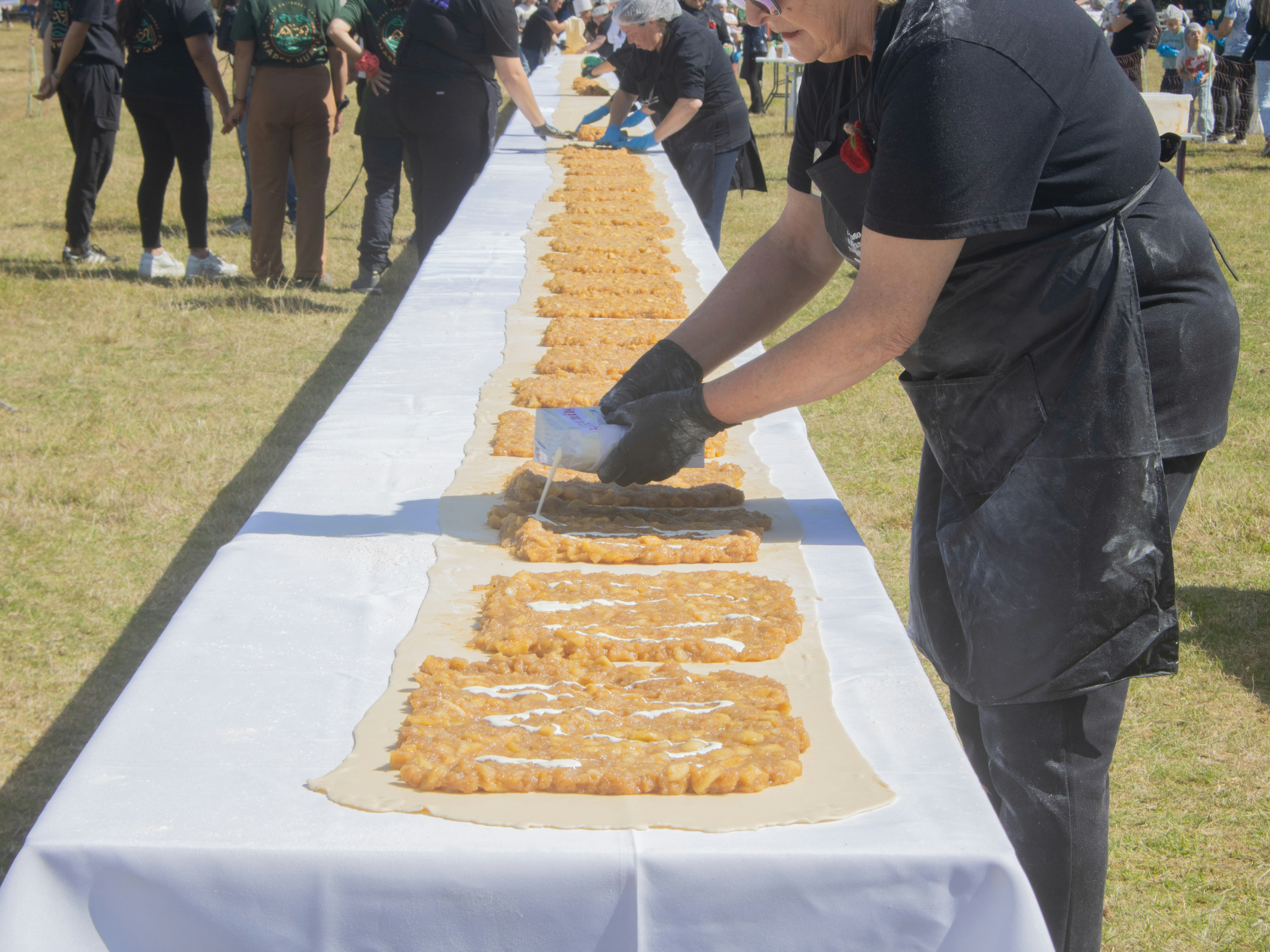 Woman prepares rectangular food on a long table.
