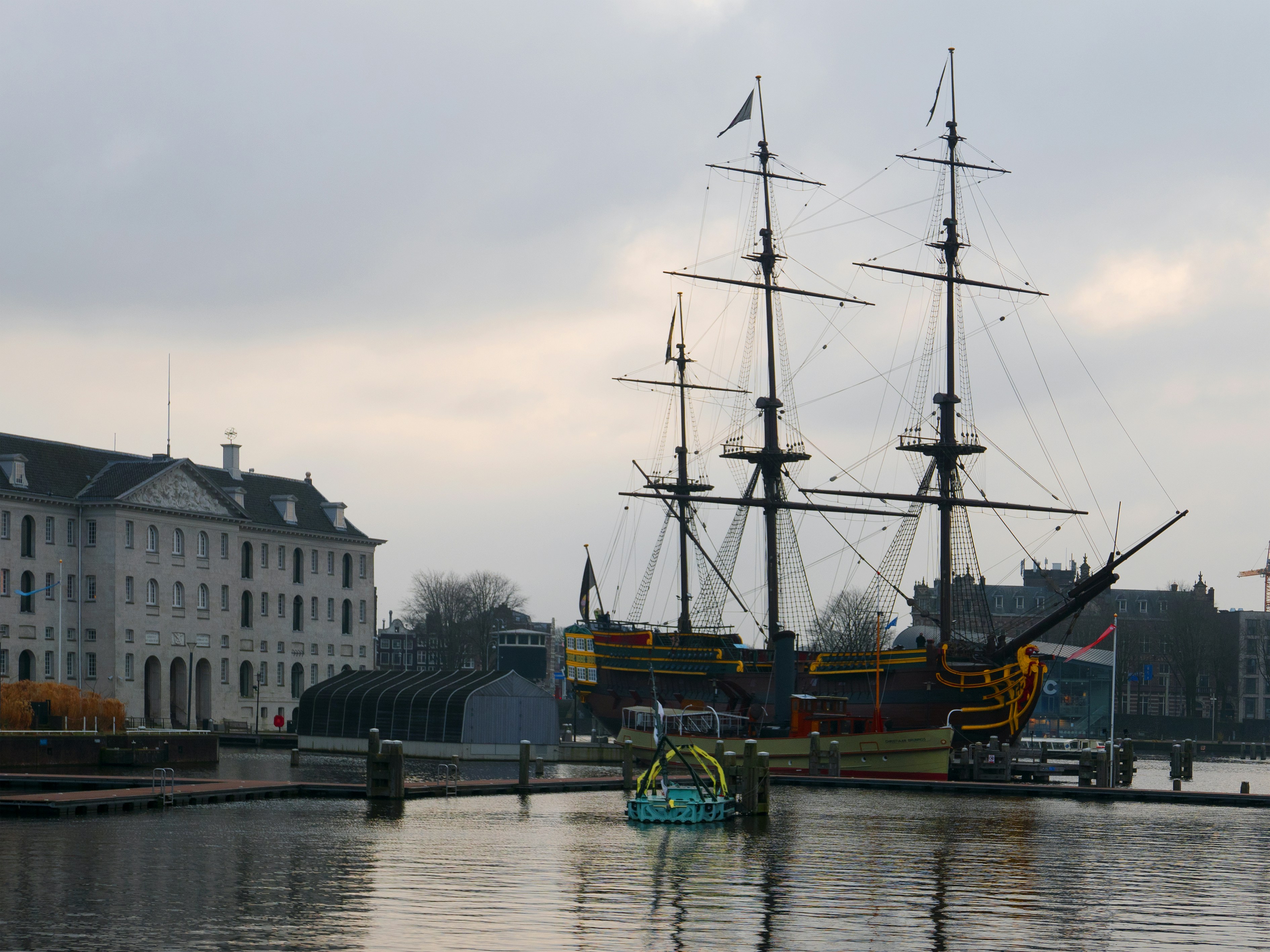 Free photo of a replica of an old maritime ship / bark is drifting in the harbour Oosterdok in Amsterdam, close to the historic store building of the Maritime Museum; photography of The Netherlands in Dutch photos. free download images in high resolutions. Foto van de Amsterdam - replica van een 17e eeuws V.O.C. schip - die drijft in het water van het Oosterdok in Amsterdam, naast het Scheepvaartmuseum; fotografie van Nederland in hoge resolutie en gratis download door fotograaf Fons Heijnsbroek.