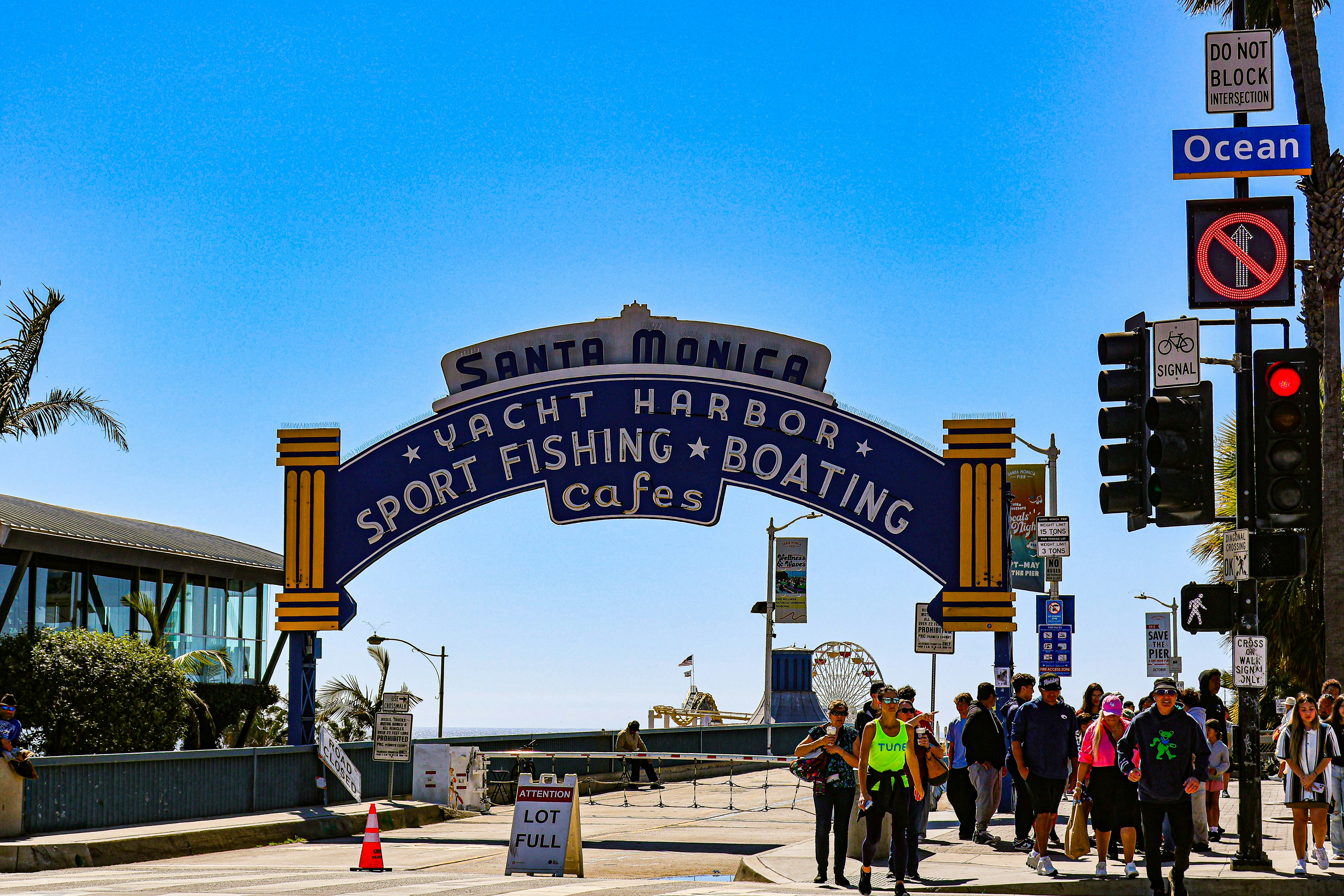 Iconic entrance archway to Santa Monica Pier with people walking under a clear blue sky.