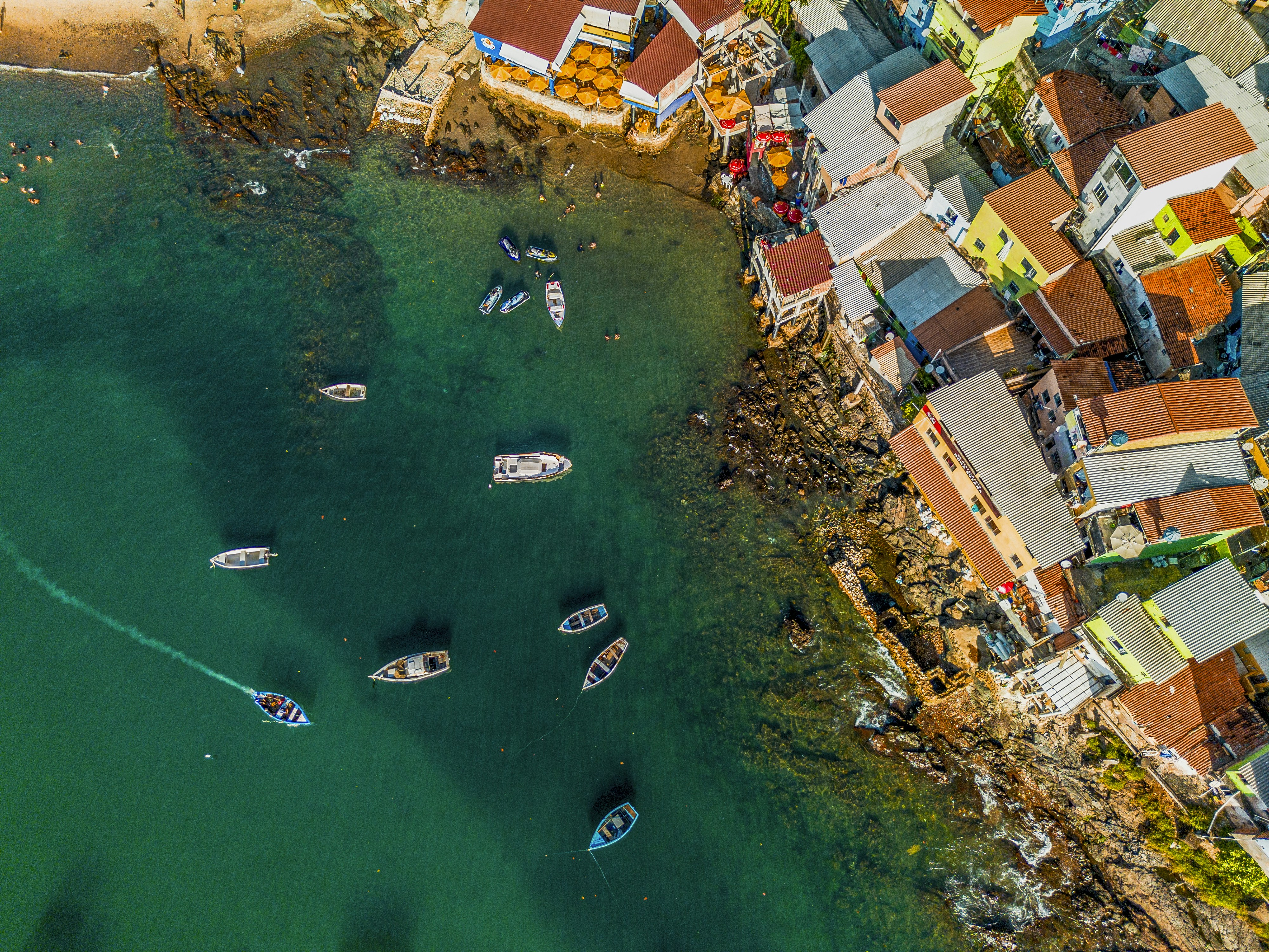 Aerial view of boats in turquoise waters alongside vibrant seaside houses.