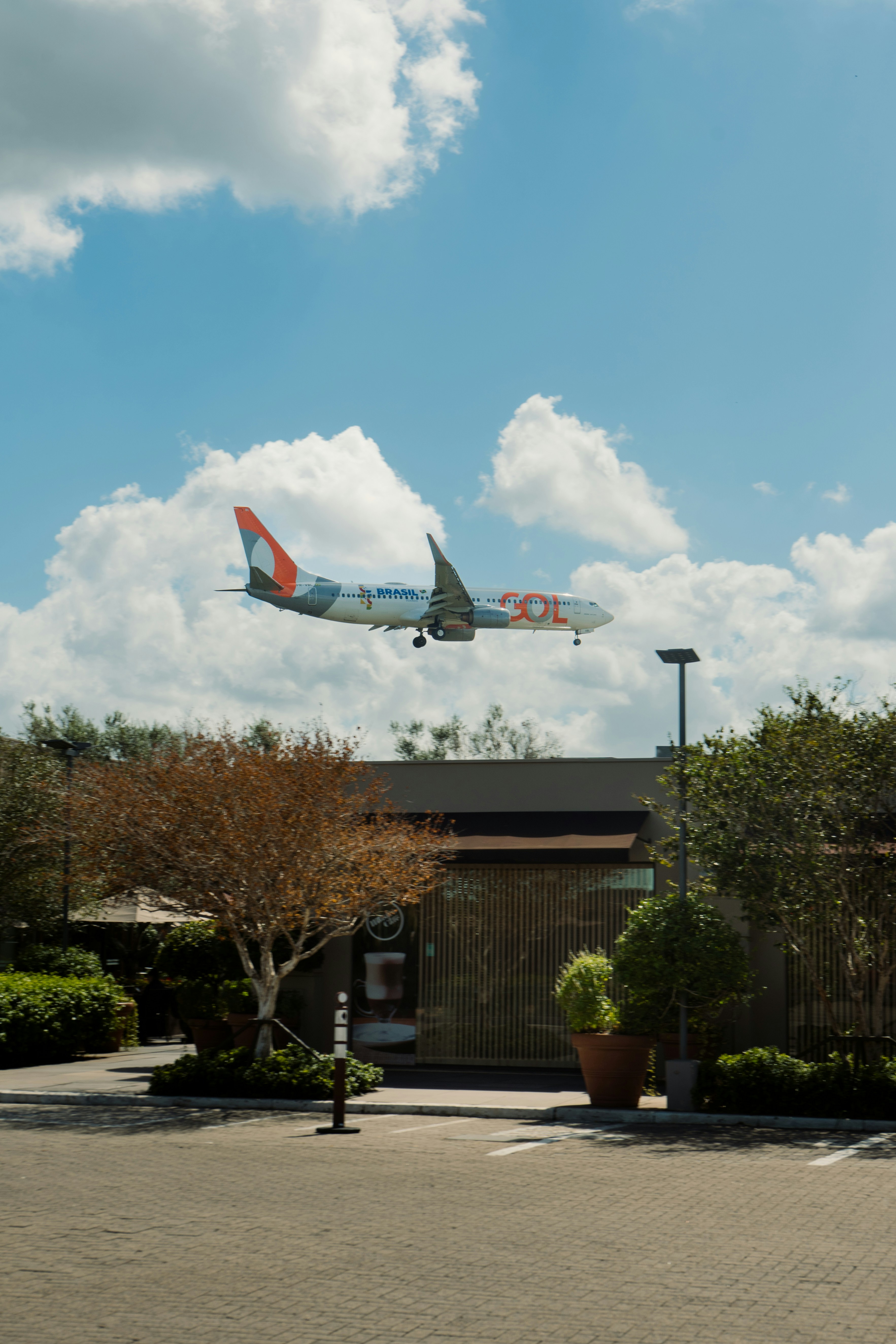 Commercial airplane flying low over a suburban area under a bright blue sky with scattered clouds.