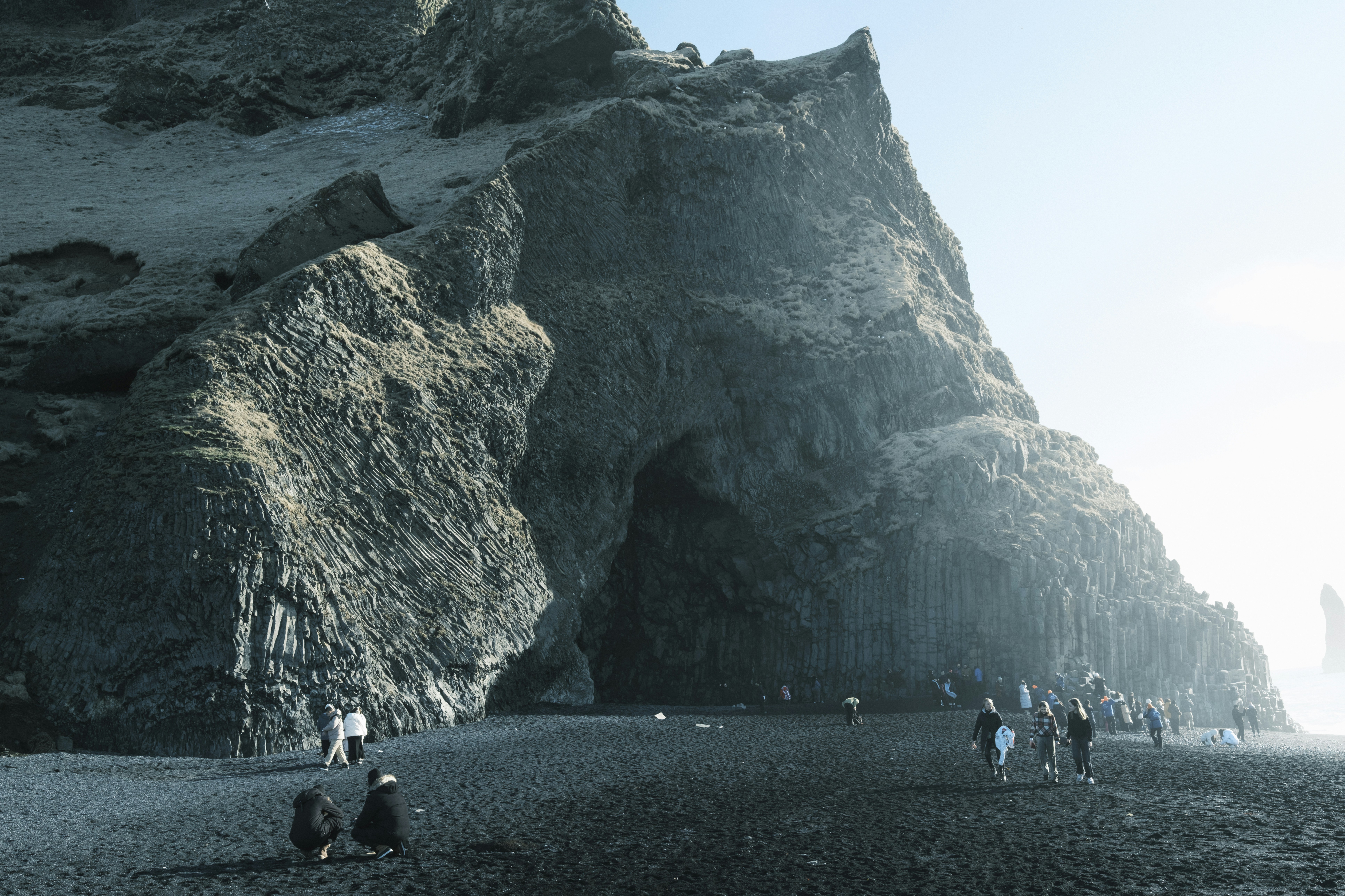 People explore a dramatic rock formation on the beach. photo – Free ...