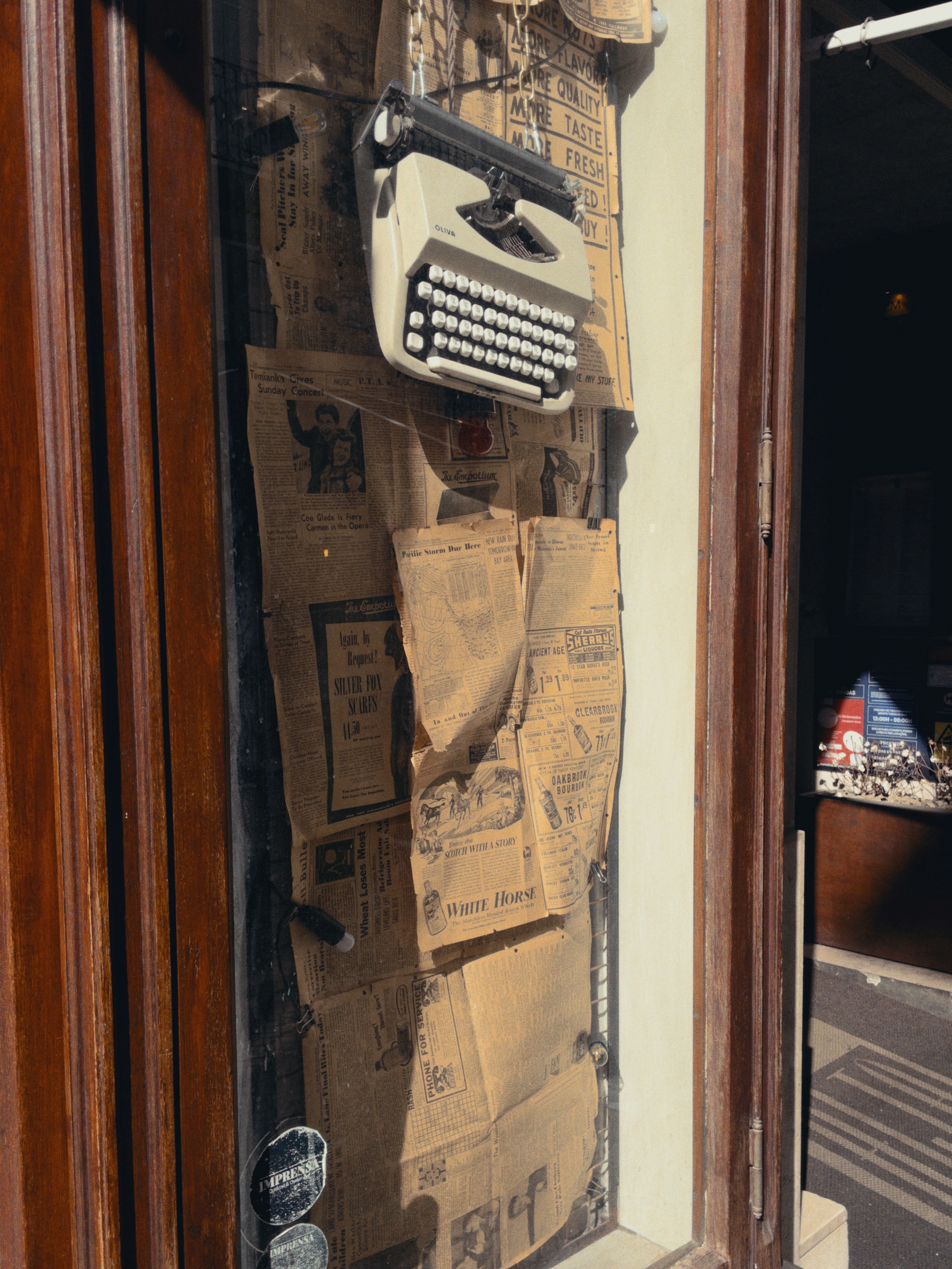 Vintage typewriter mounted on a window with newspaper clippings, evoking nostalgia and the art of writing.