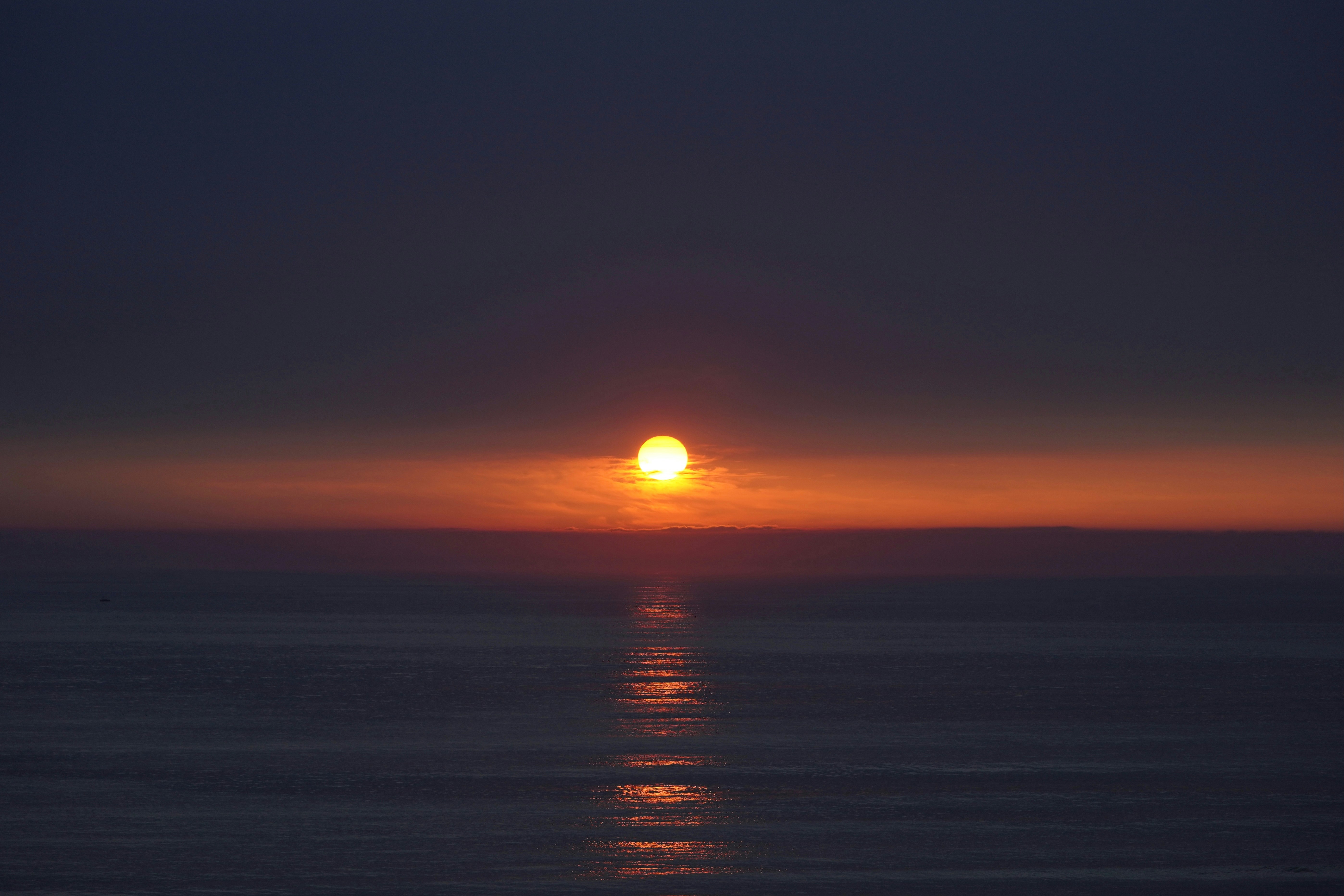Sunset casting warm hues over a calm ocean, with the sun partially obscured by a darkening sky.