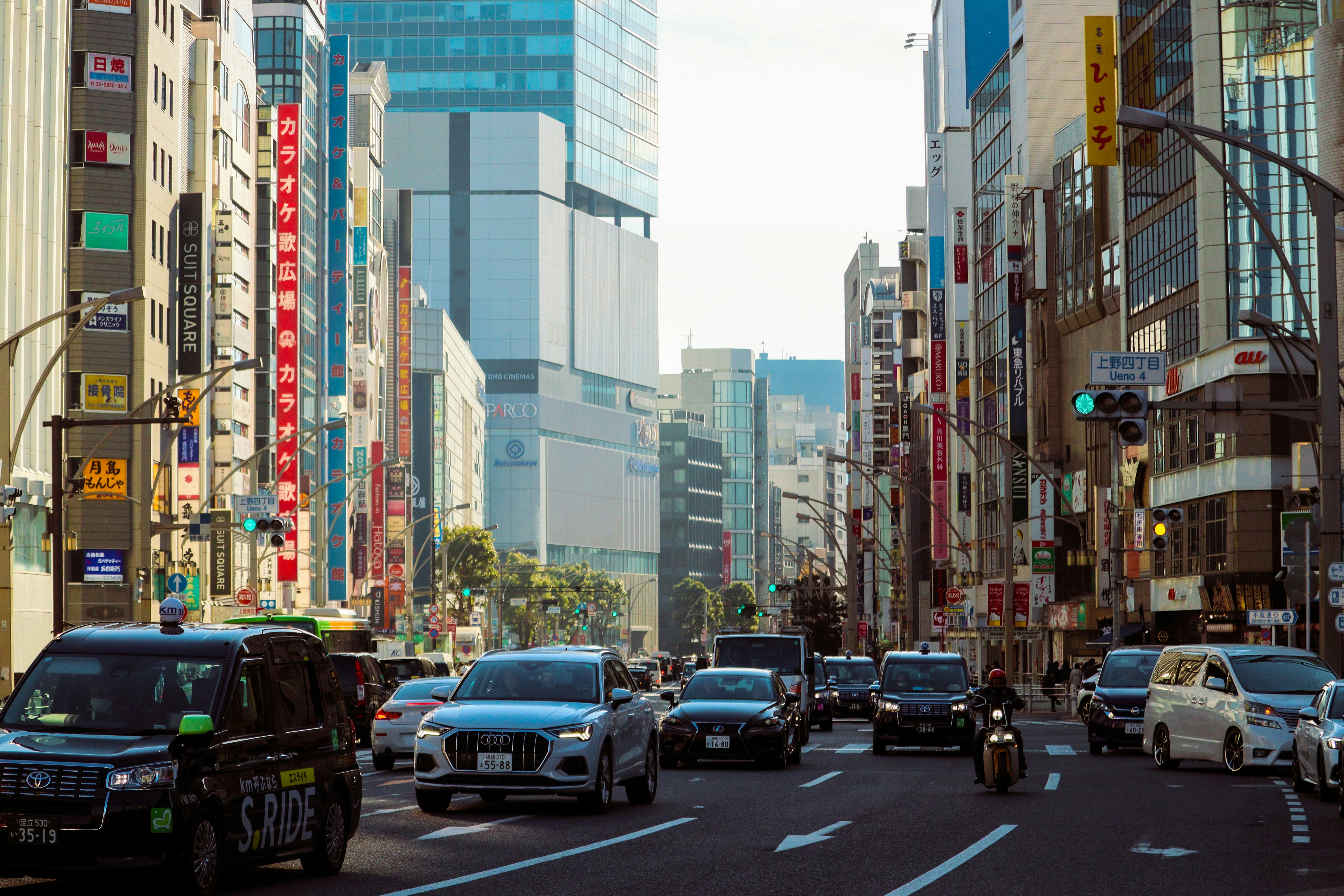 Vibrant cityscape with cars and motorcycles navigating a busy Tokyo street lined with towering buildings and colorful signs.