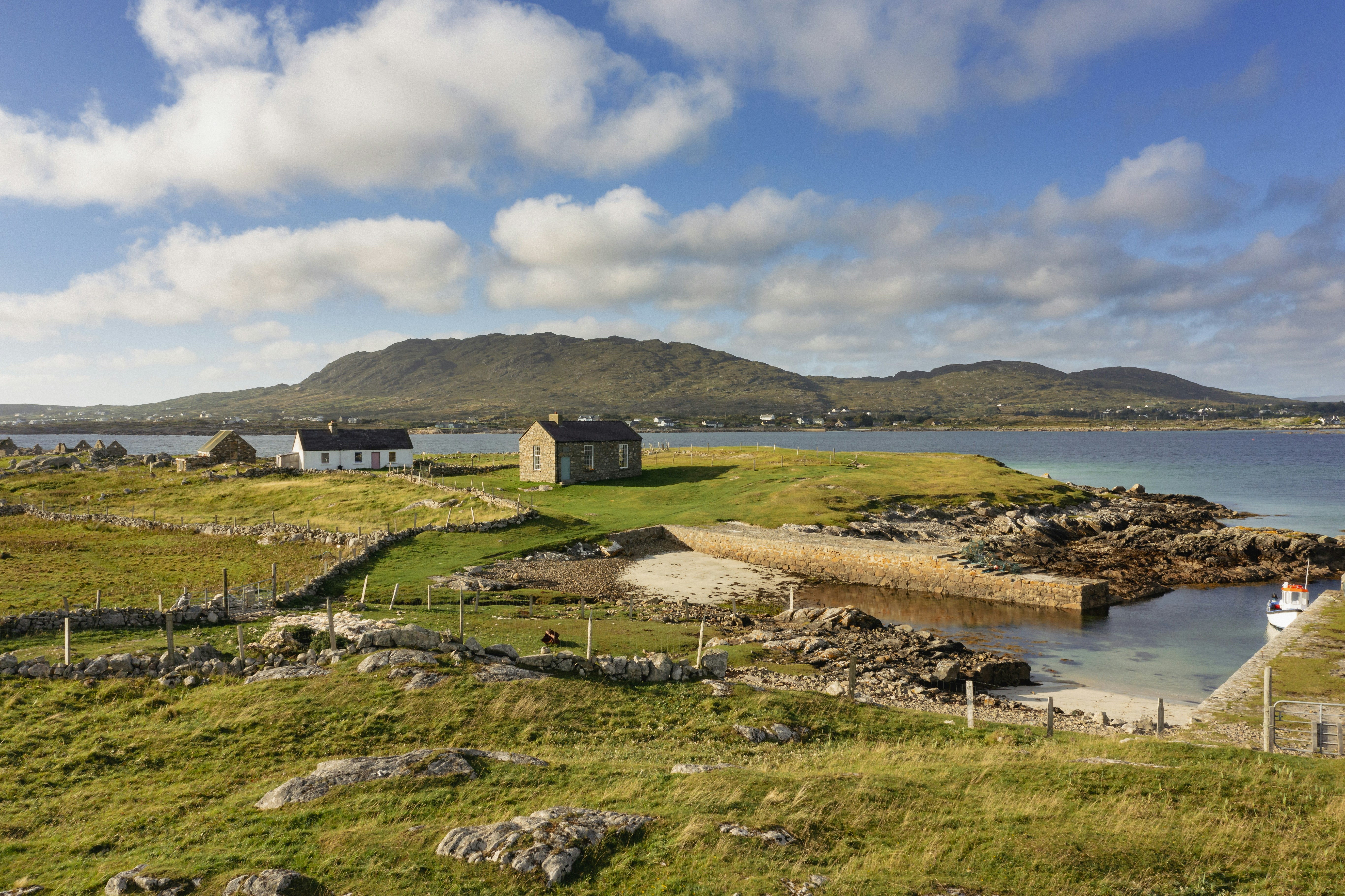 Traditional stone cottages by a tranquil harbor with rolling hills and the Atlantic Ocean in the background.