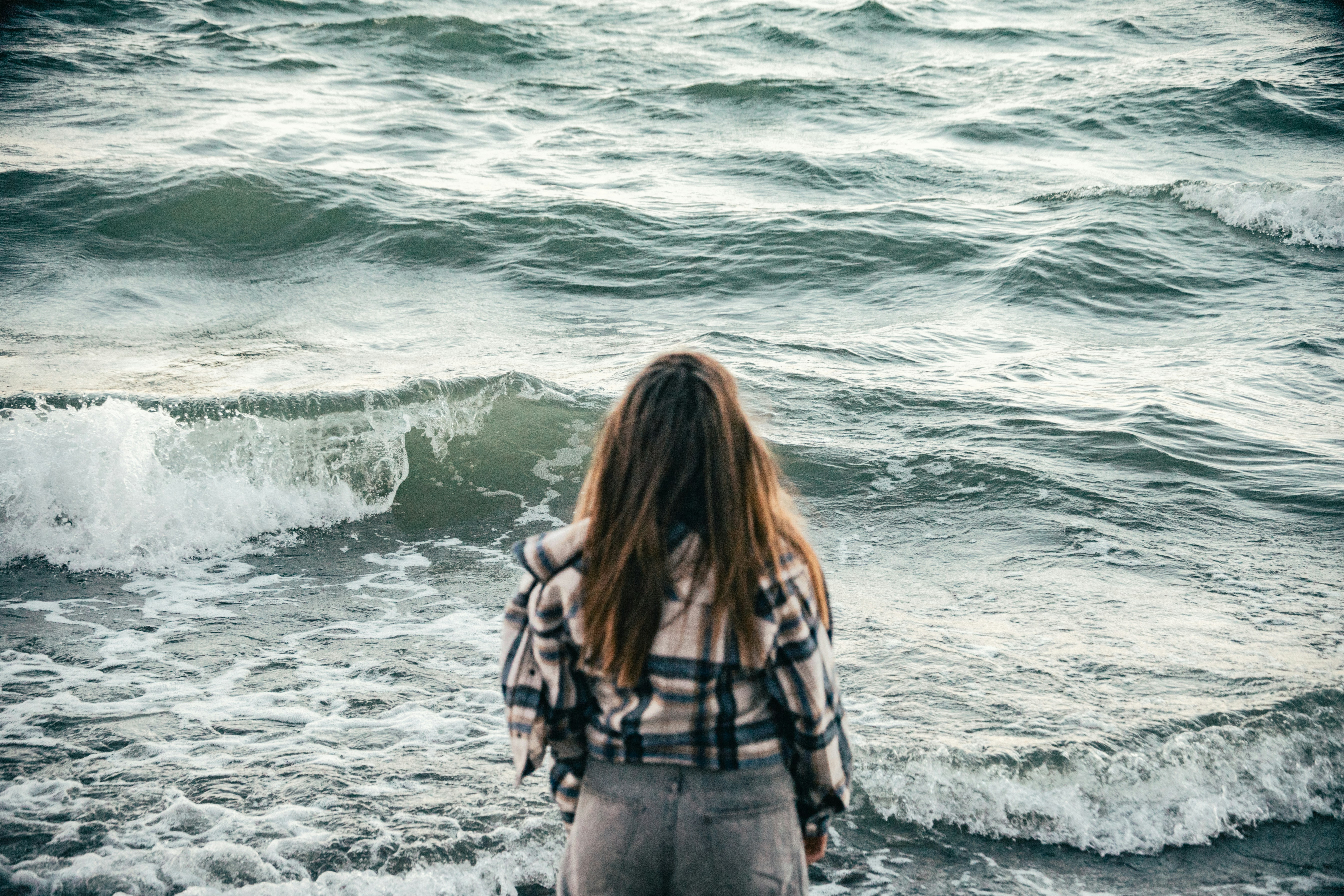 Person in plaid jacket gazes at crashing ocean waves.