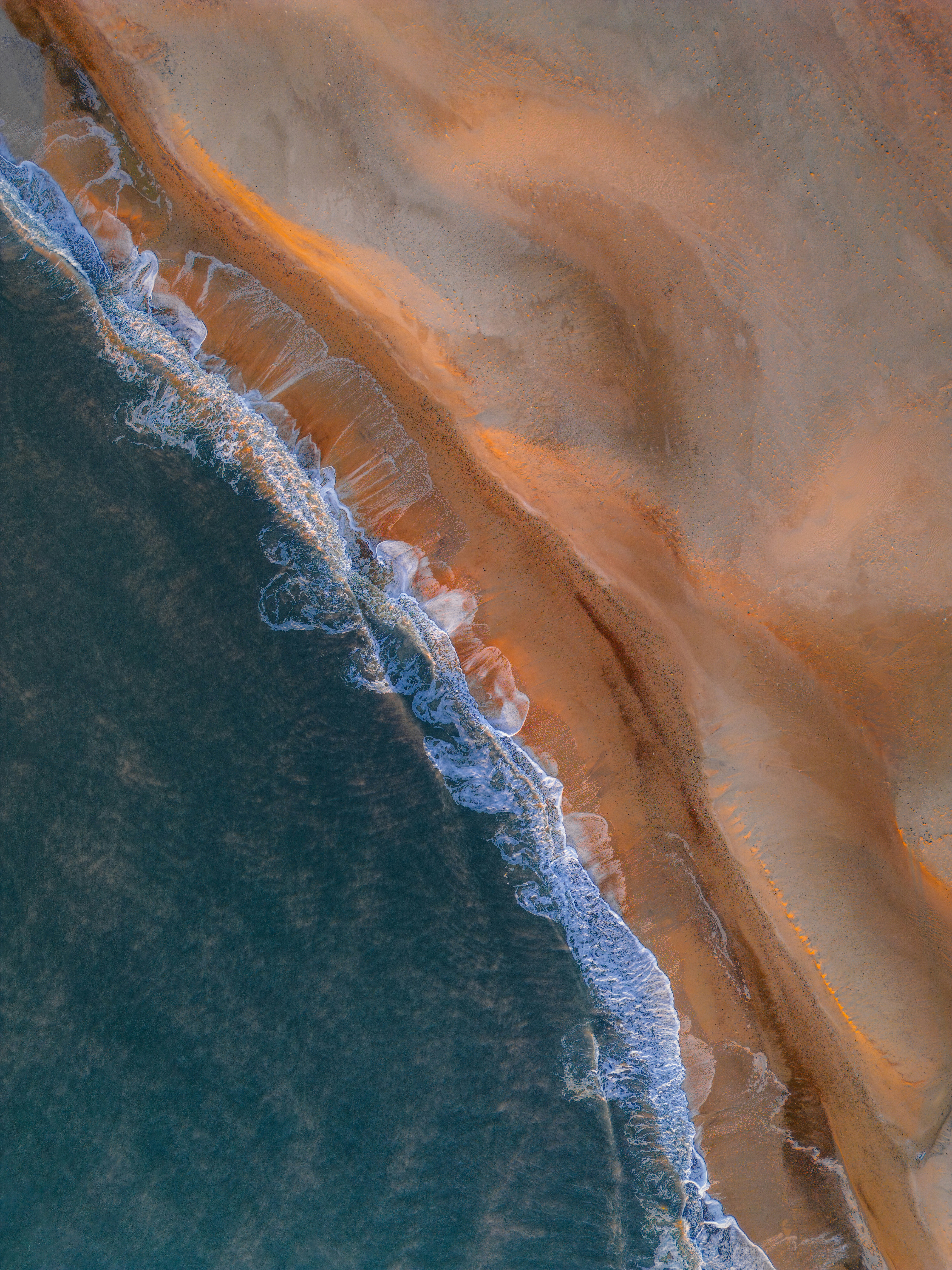 Aerial view of ocean waves meeting a sandy shoreline with rich earthy tones.