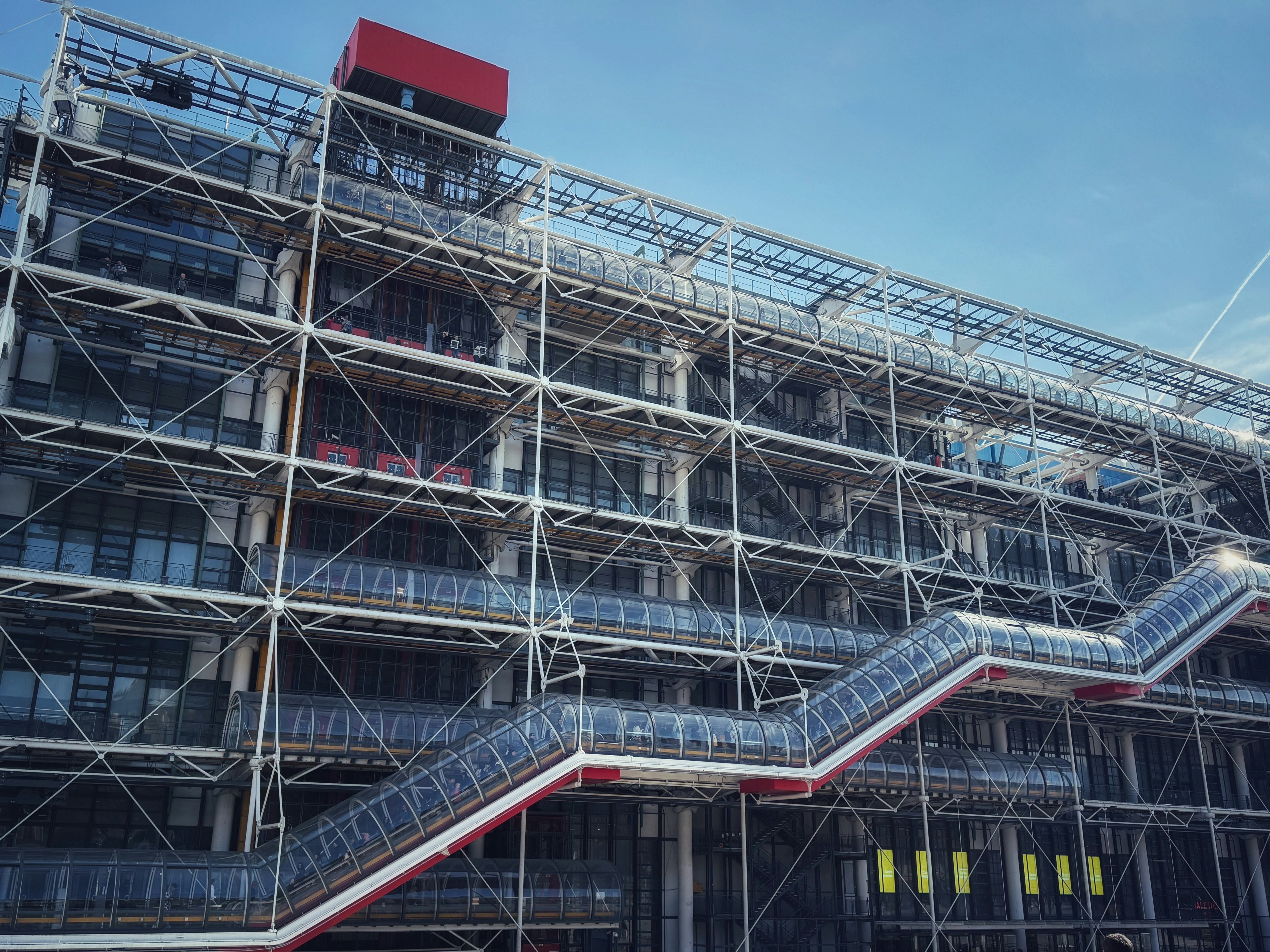 Exposed structural framework of the Centre Pompidou against a clear blue sky.