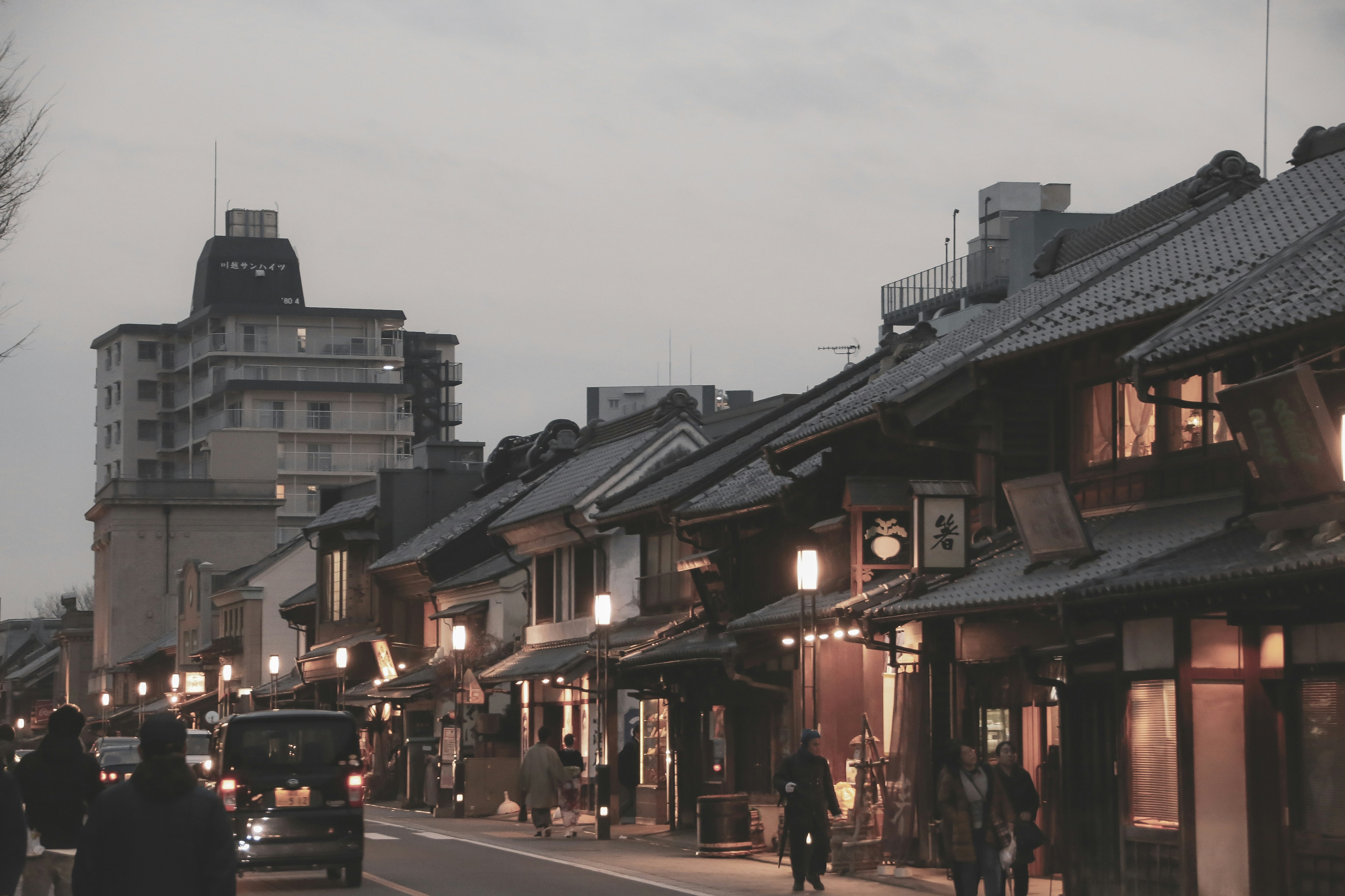 Traditional Japanese buildings line a street at dusk, softly illuminated by warm lights.
