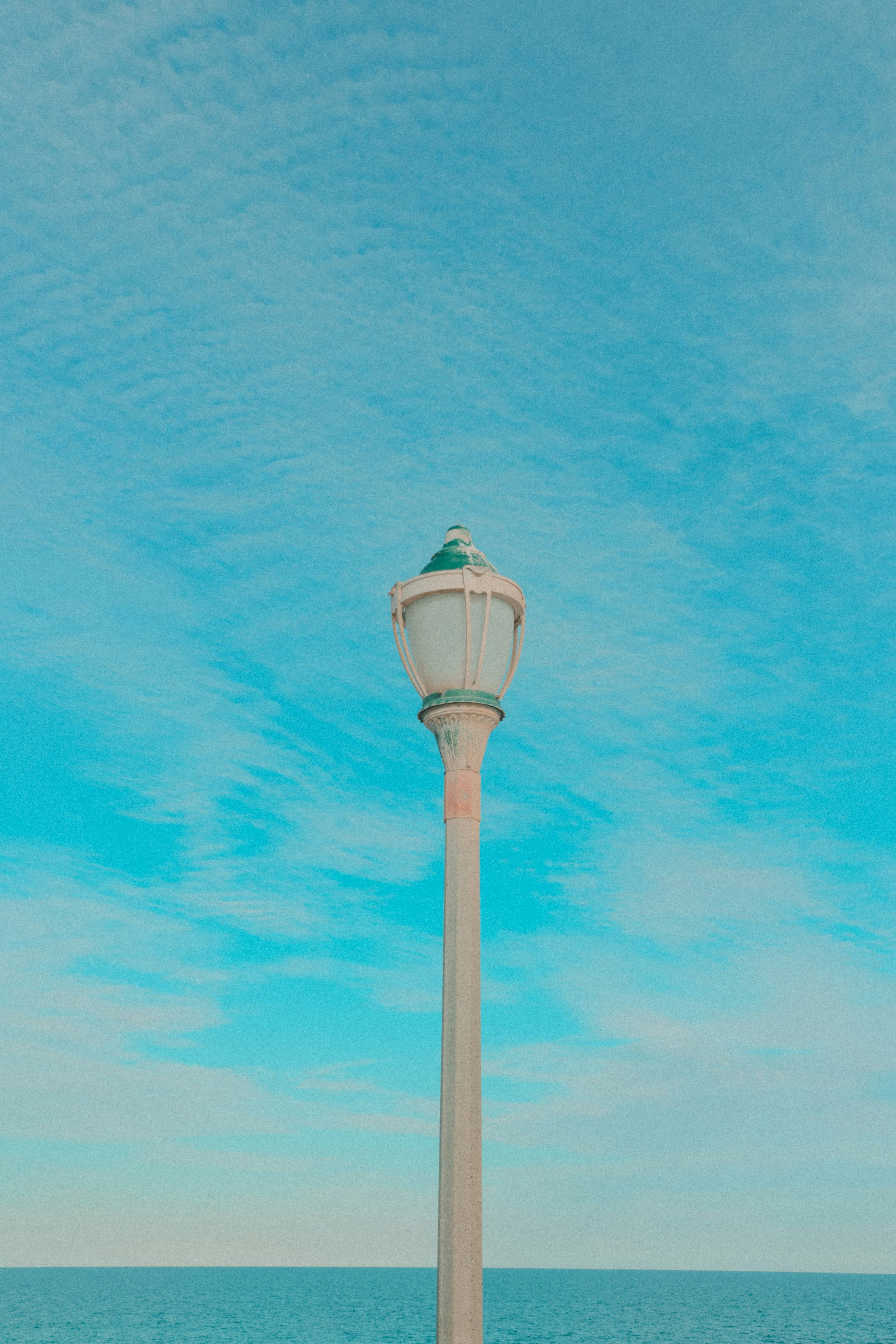 A vintage lamp post stands tall against a serene blue sky and calm ocean backdrop.