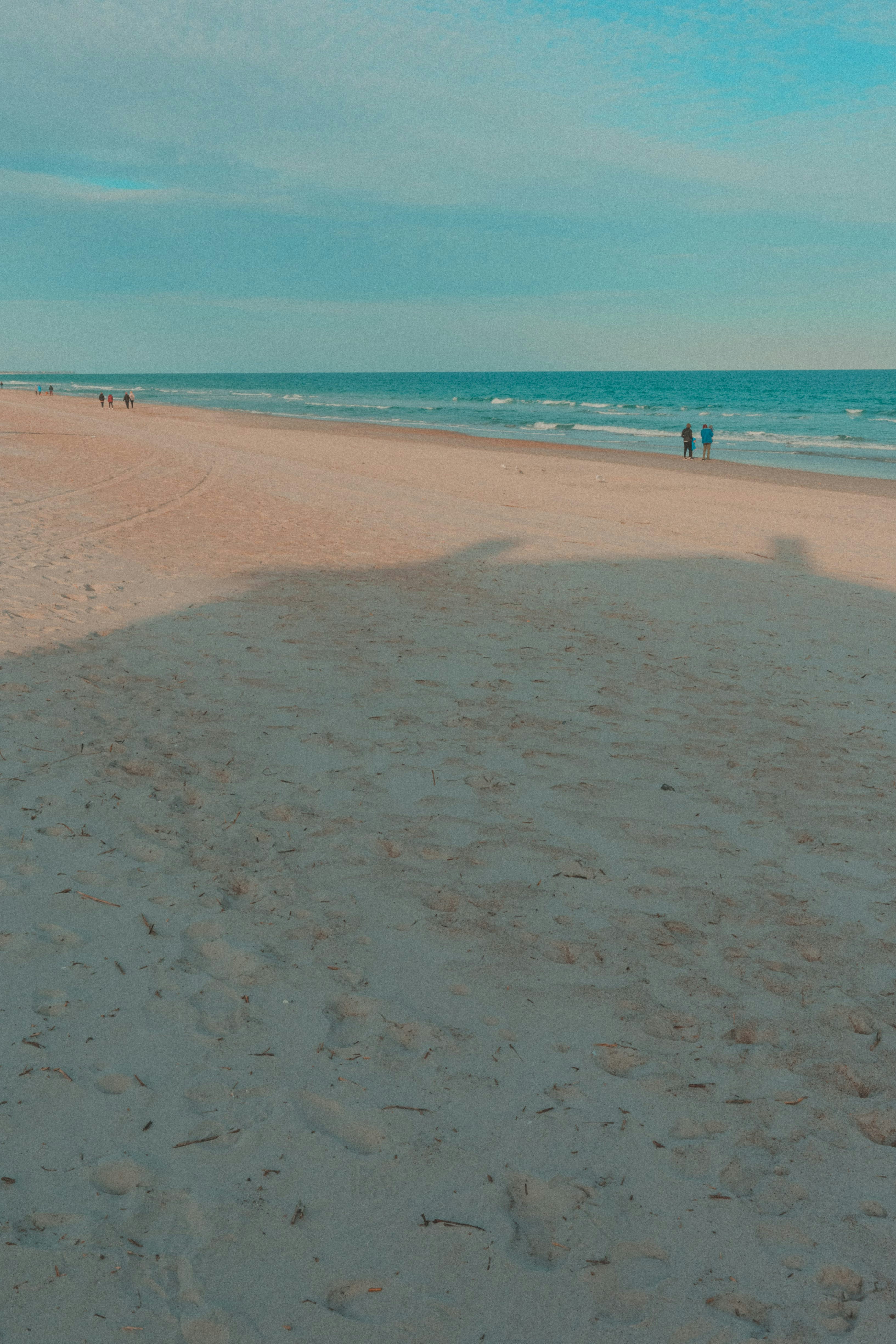 Expansive sandy beach with a shadow stretching towards gentle waves under a clear sky.