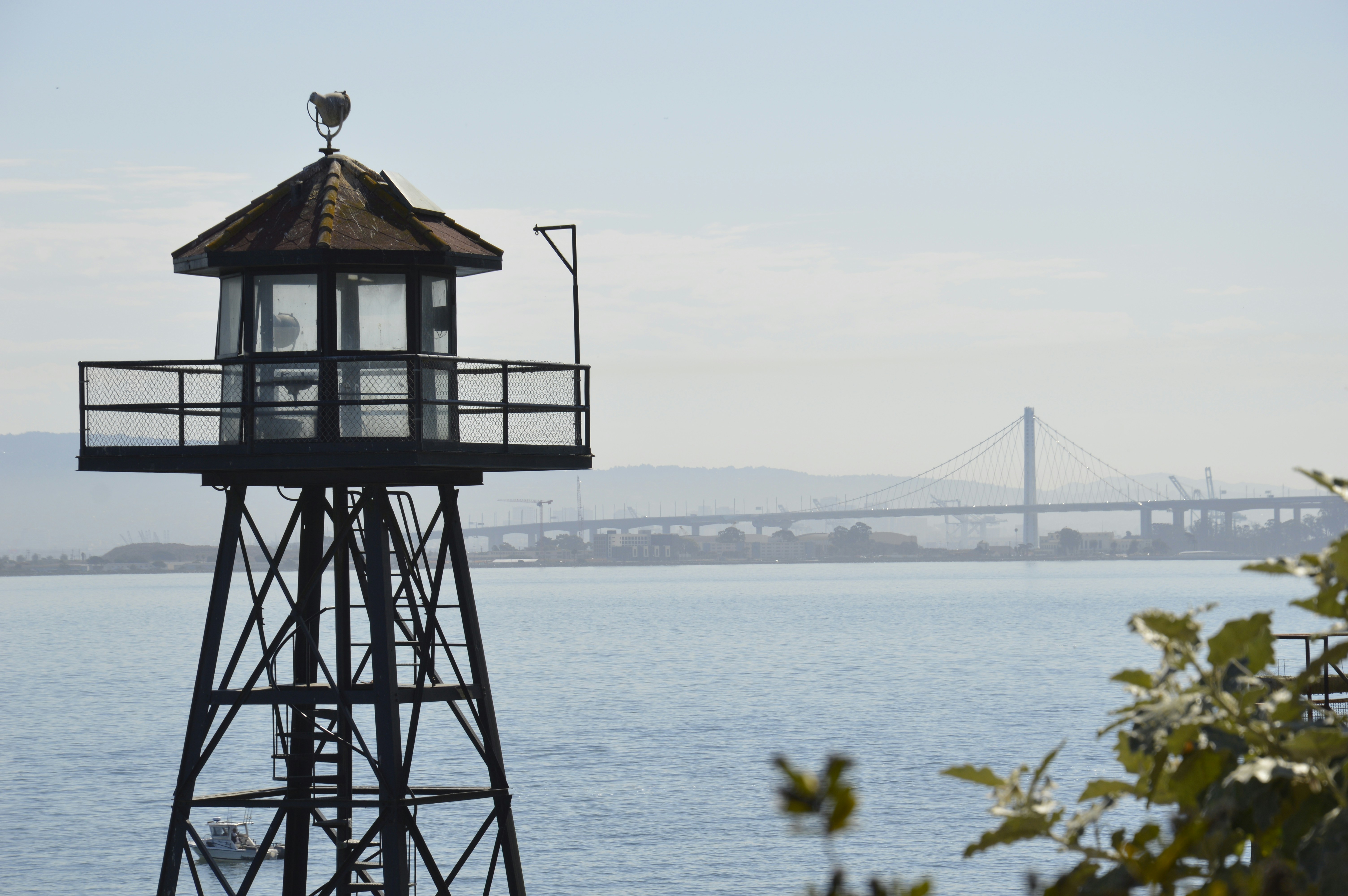 Rustic guard tower overlooking a calm bay with a distant suspension bridge under a clear sky.