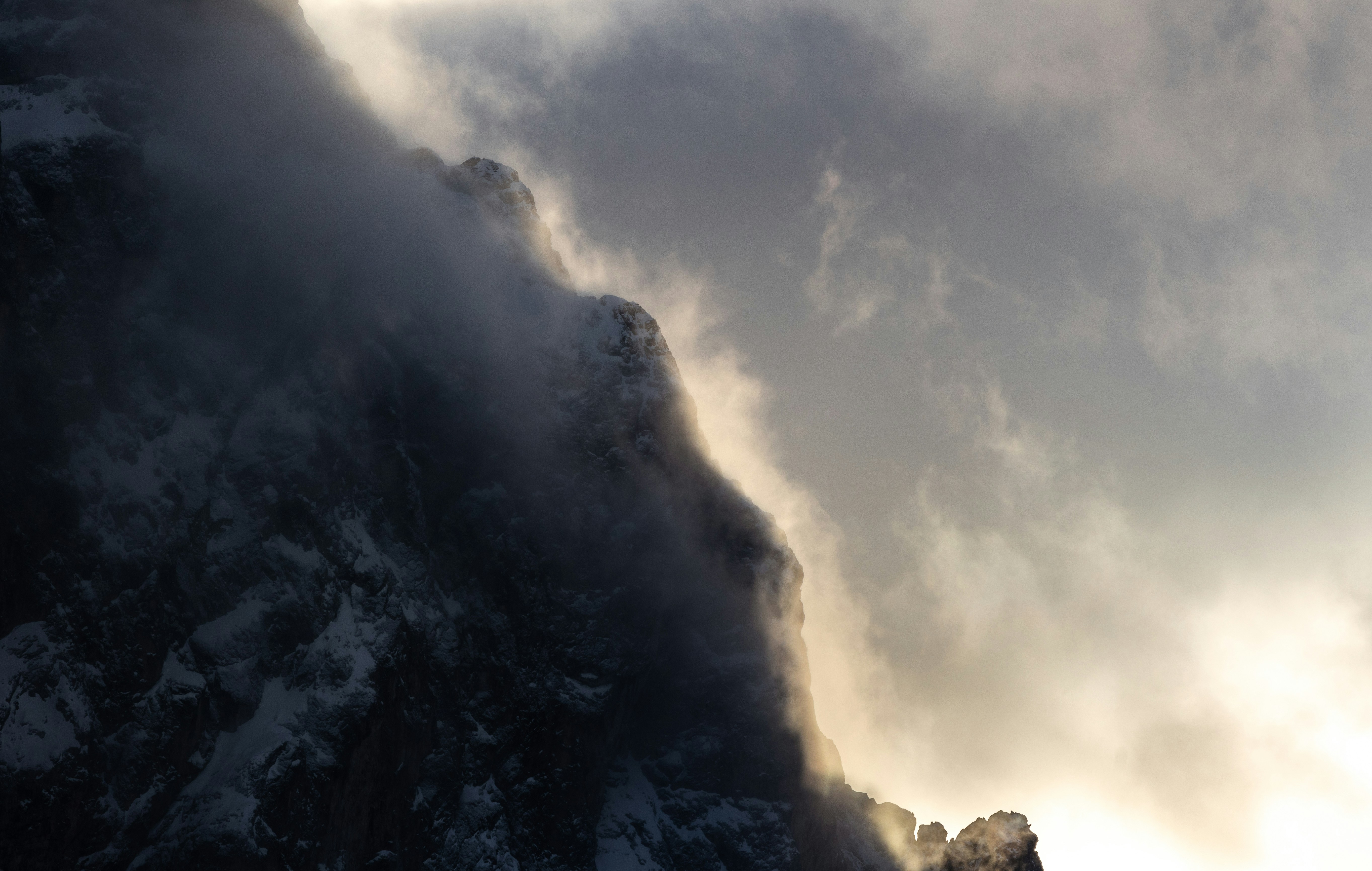 Sunlight piercing through fog enveloping a rugged mountain peak.