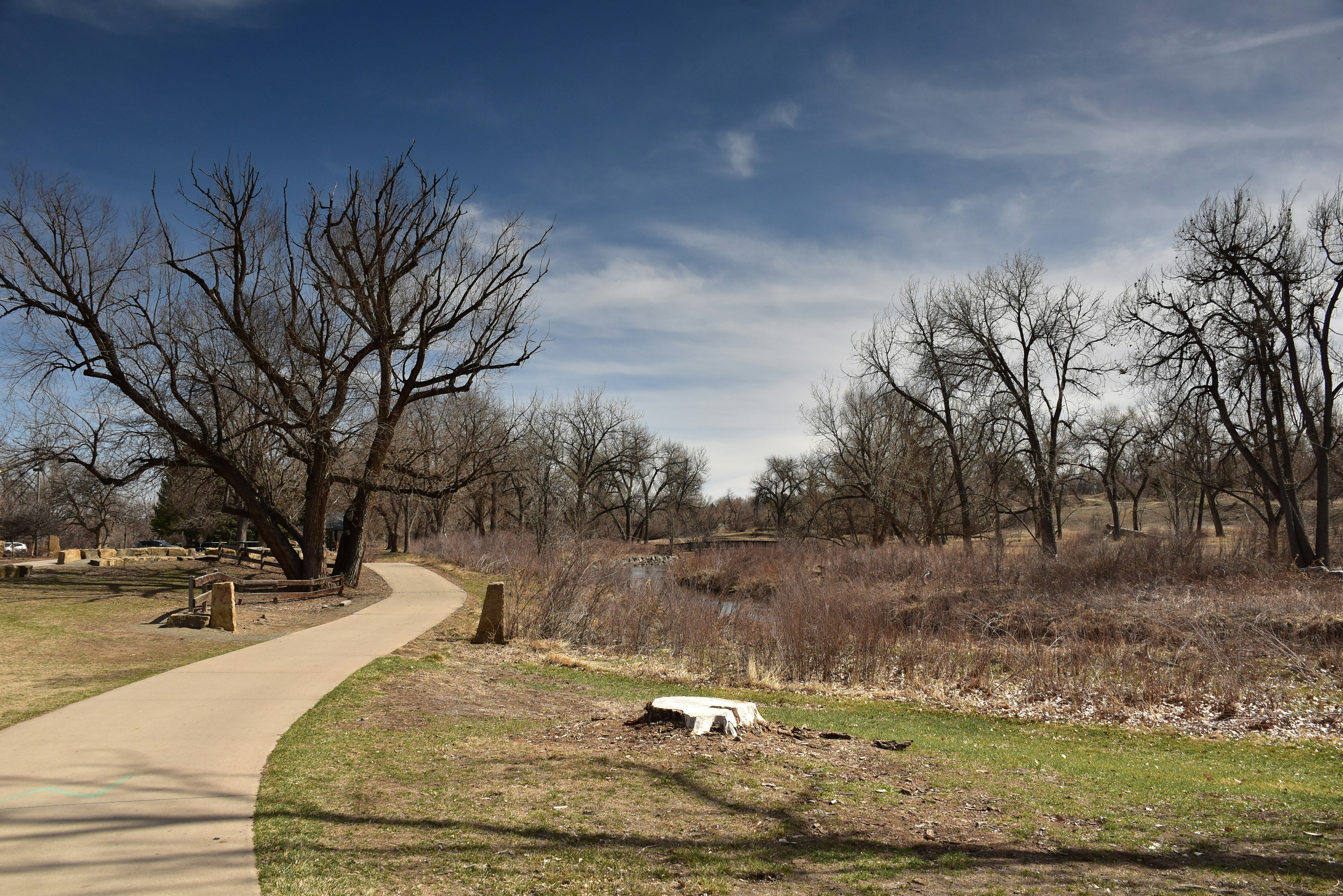 A winding path curves through a park with bare trees under a partly cloudy sky.