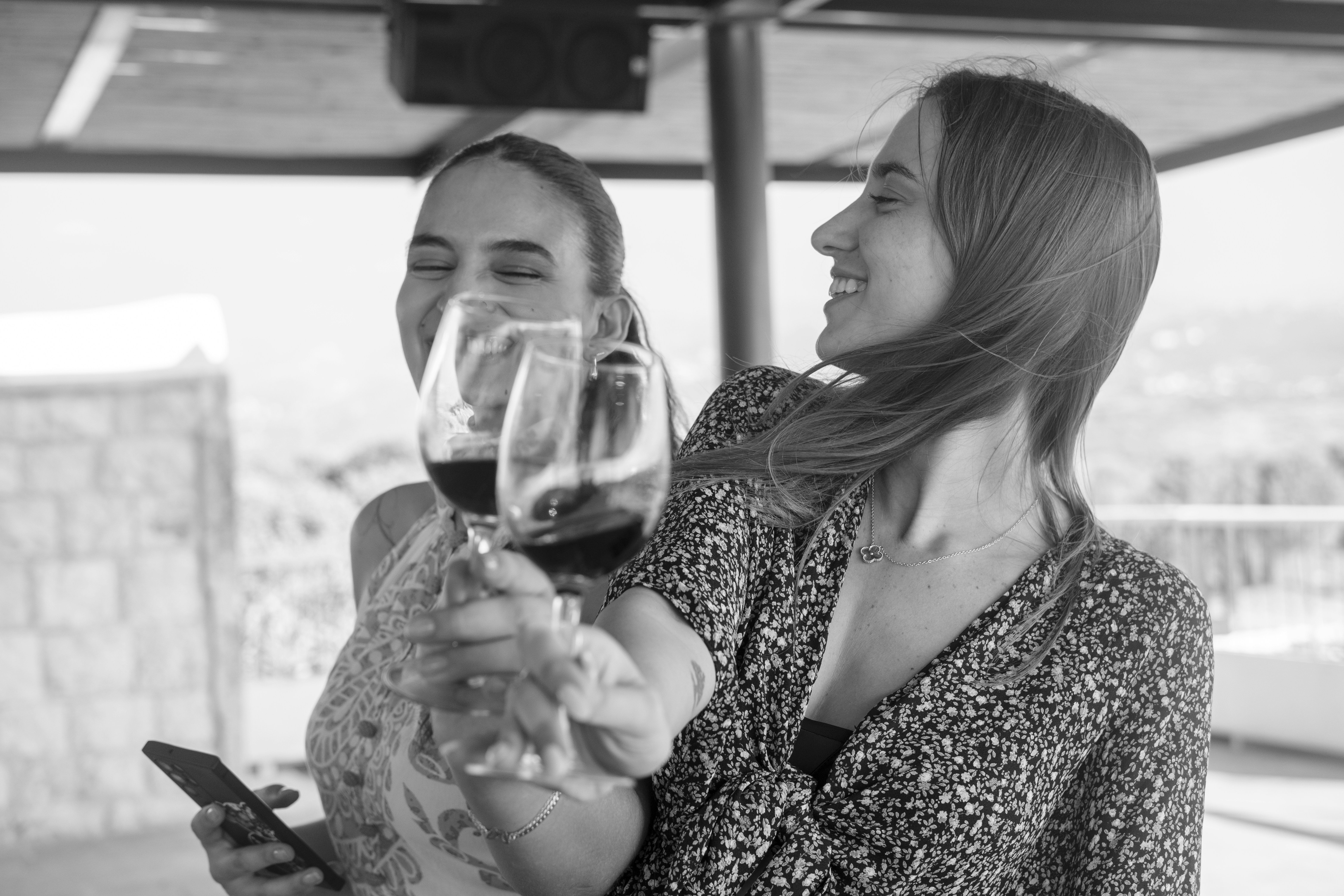 Two women clinking wine glasses while sharing a moment of laughter on a terrace.