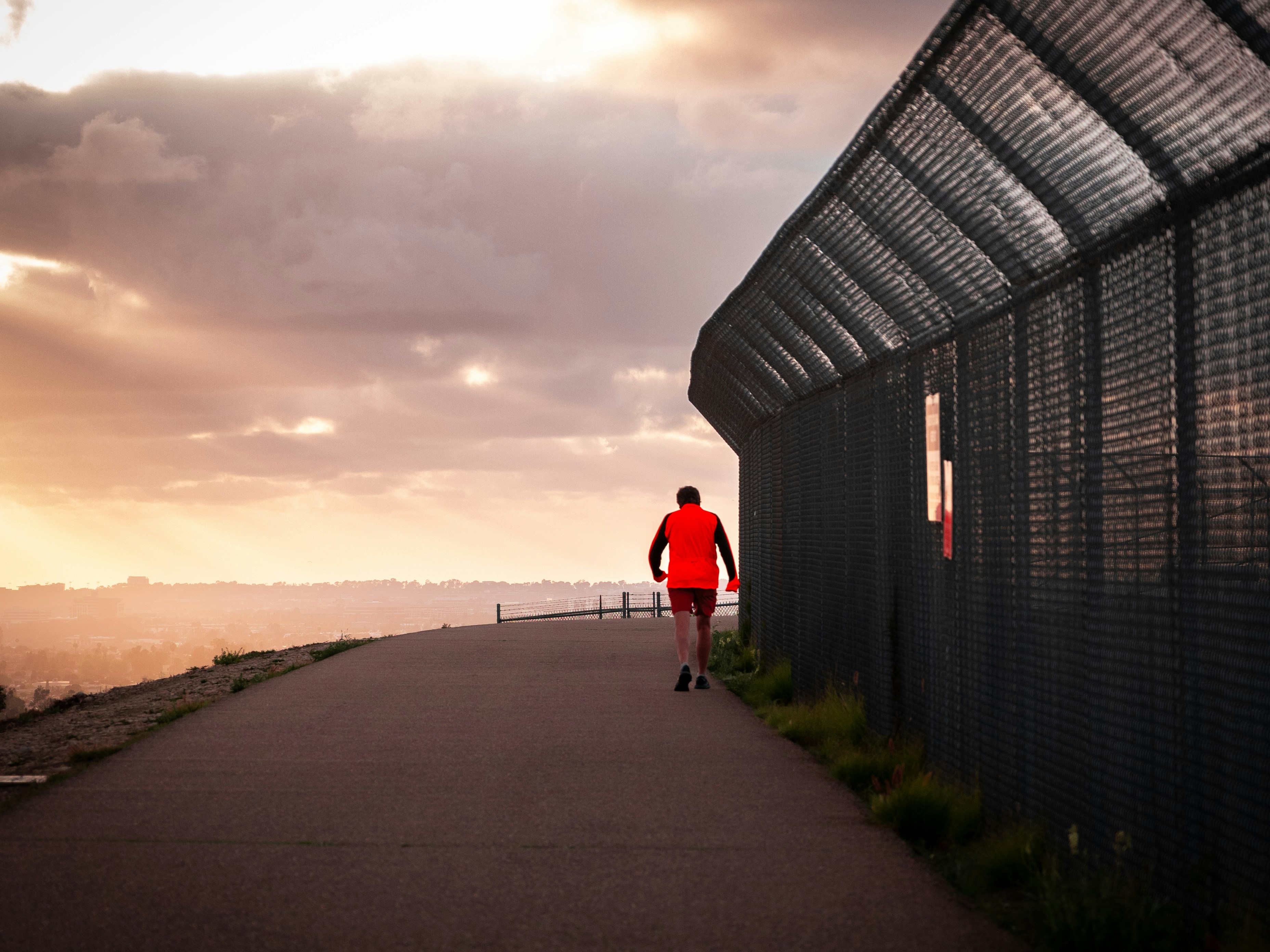A runner jogs near a fence during sunset. photo – Free City Image on ...