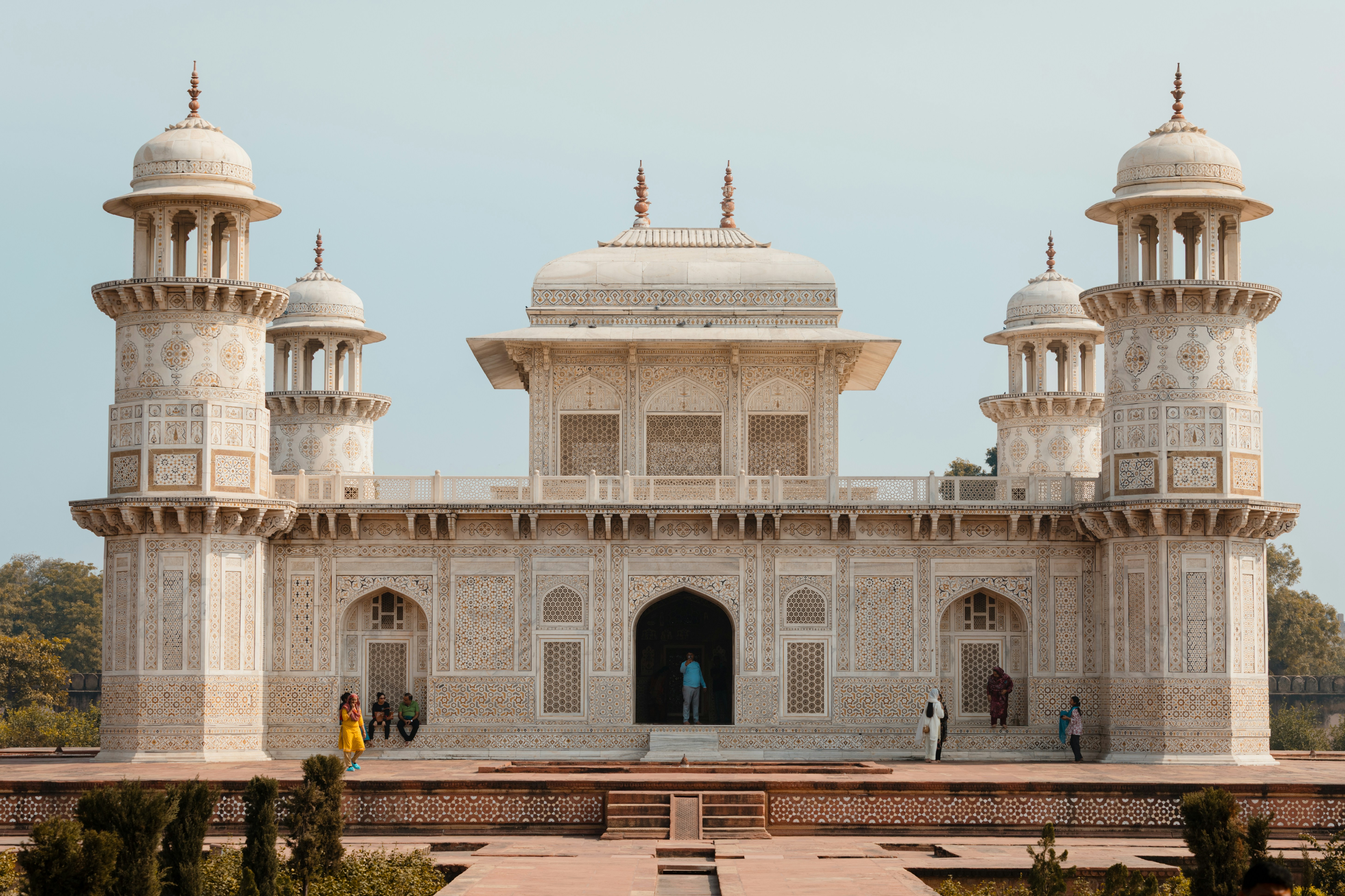 Intricately carved Mughal mausoleum with four corner towers under a clear sky.