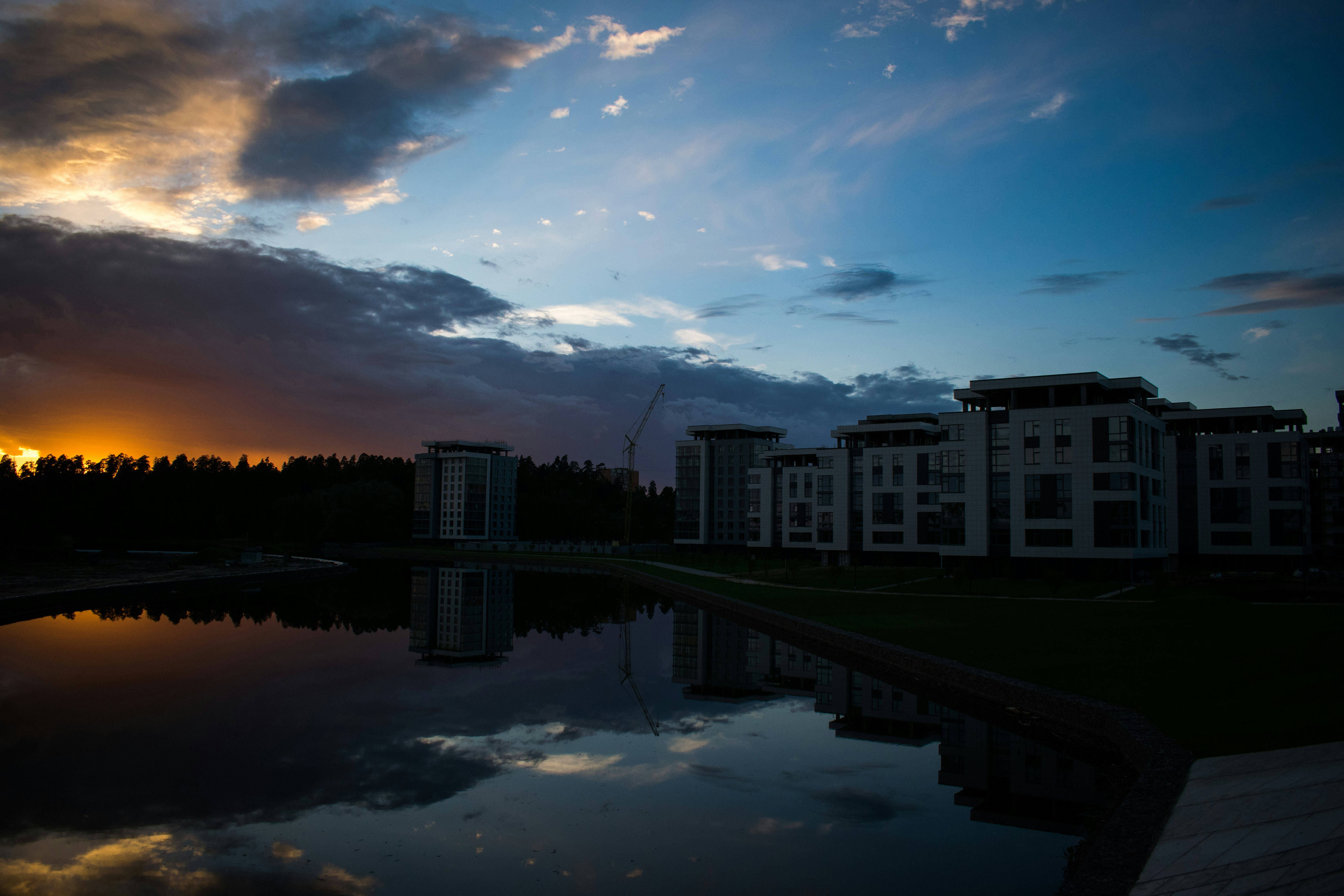 Modern buildings reflecting in calm waters at twilight, framed by a vibrant sky transitioning from day to night.