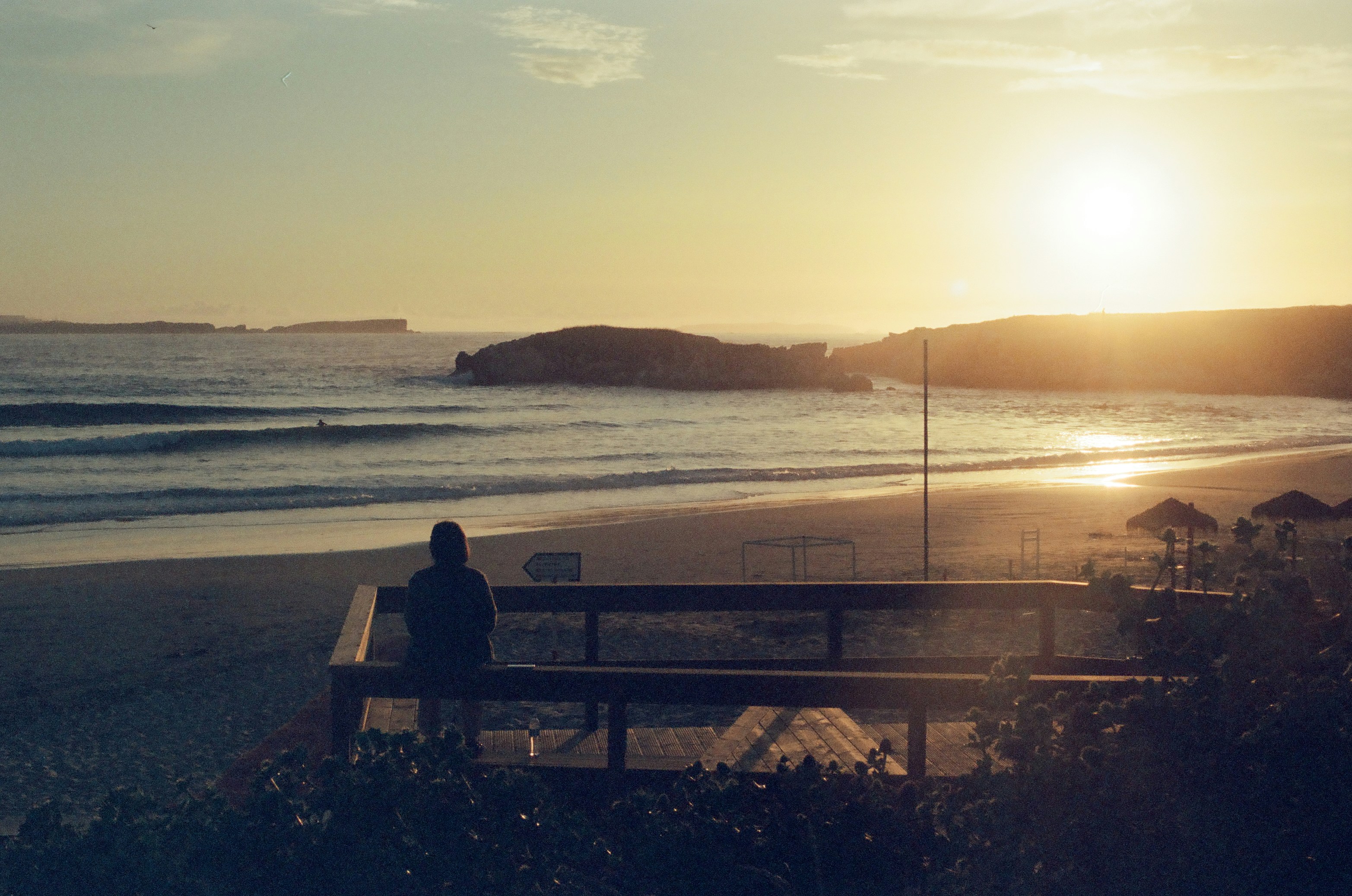 Silhouette of a person sitting on a bench, watching the sun set over a tranquil ocean.