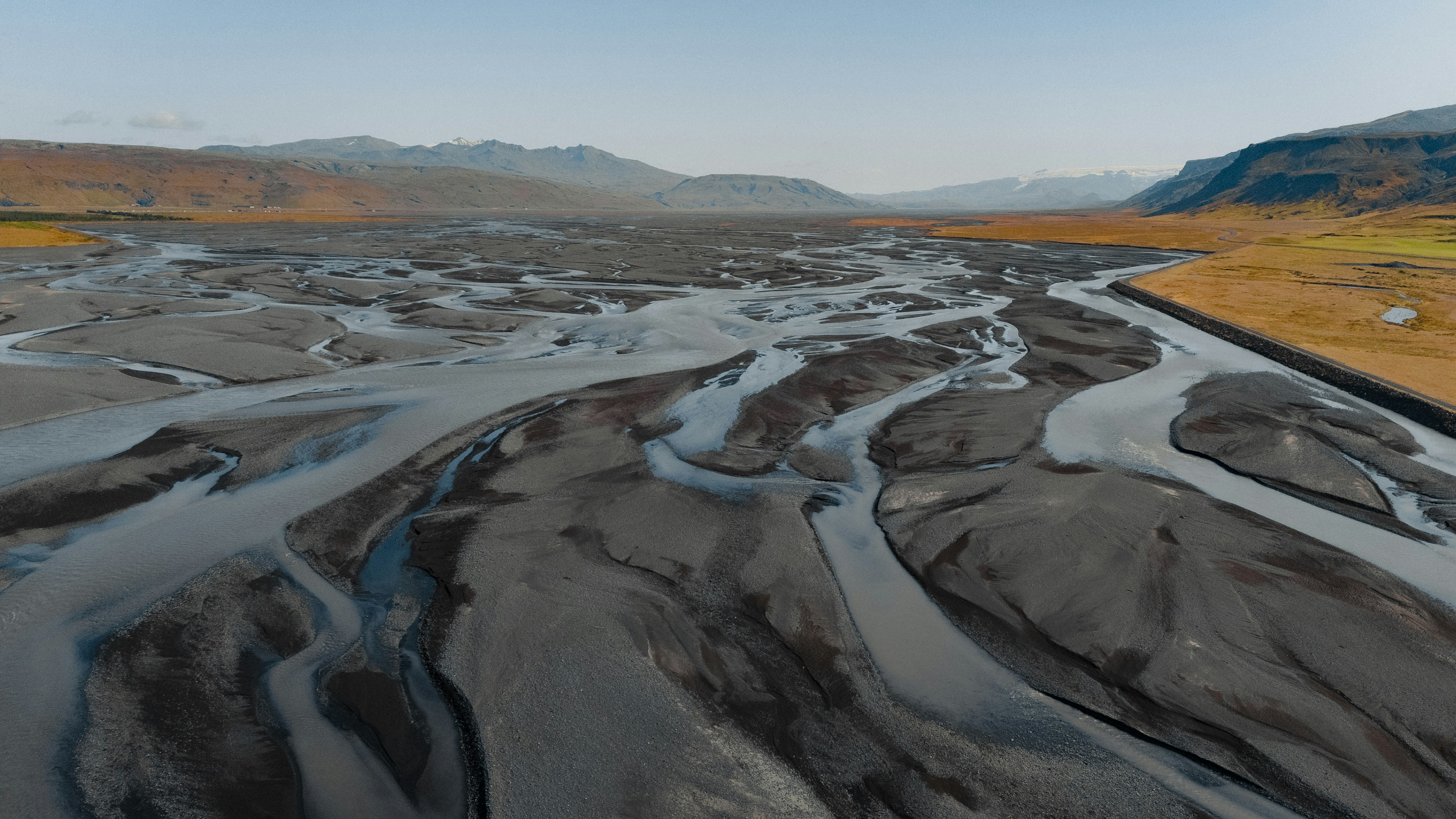 Aerial photograph of vast mudflats etched by winding water channels, with distant mountains under a clear sky.