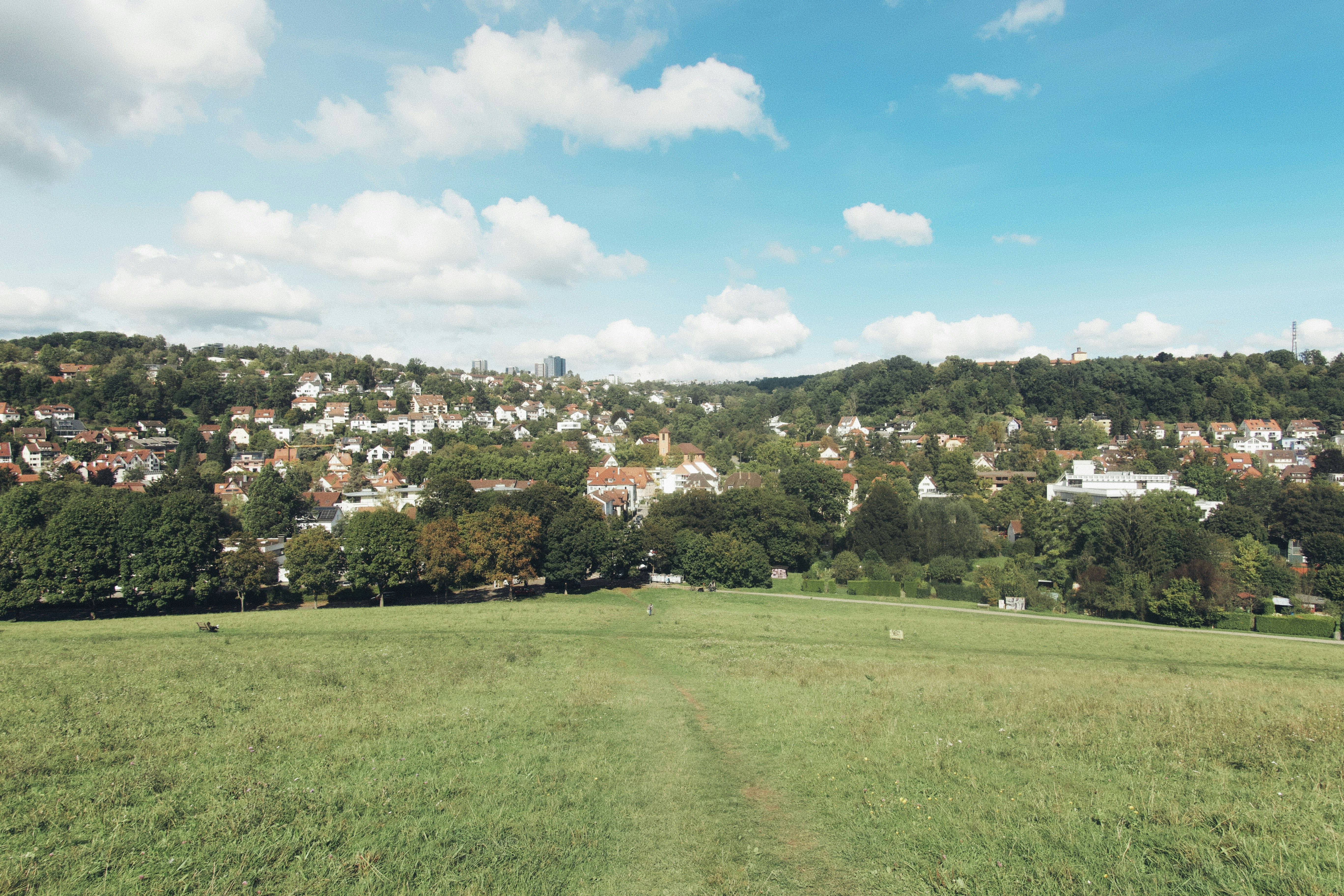 Expansive view of a cityscape nestled among lush green hills under a vivid blue sky.