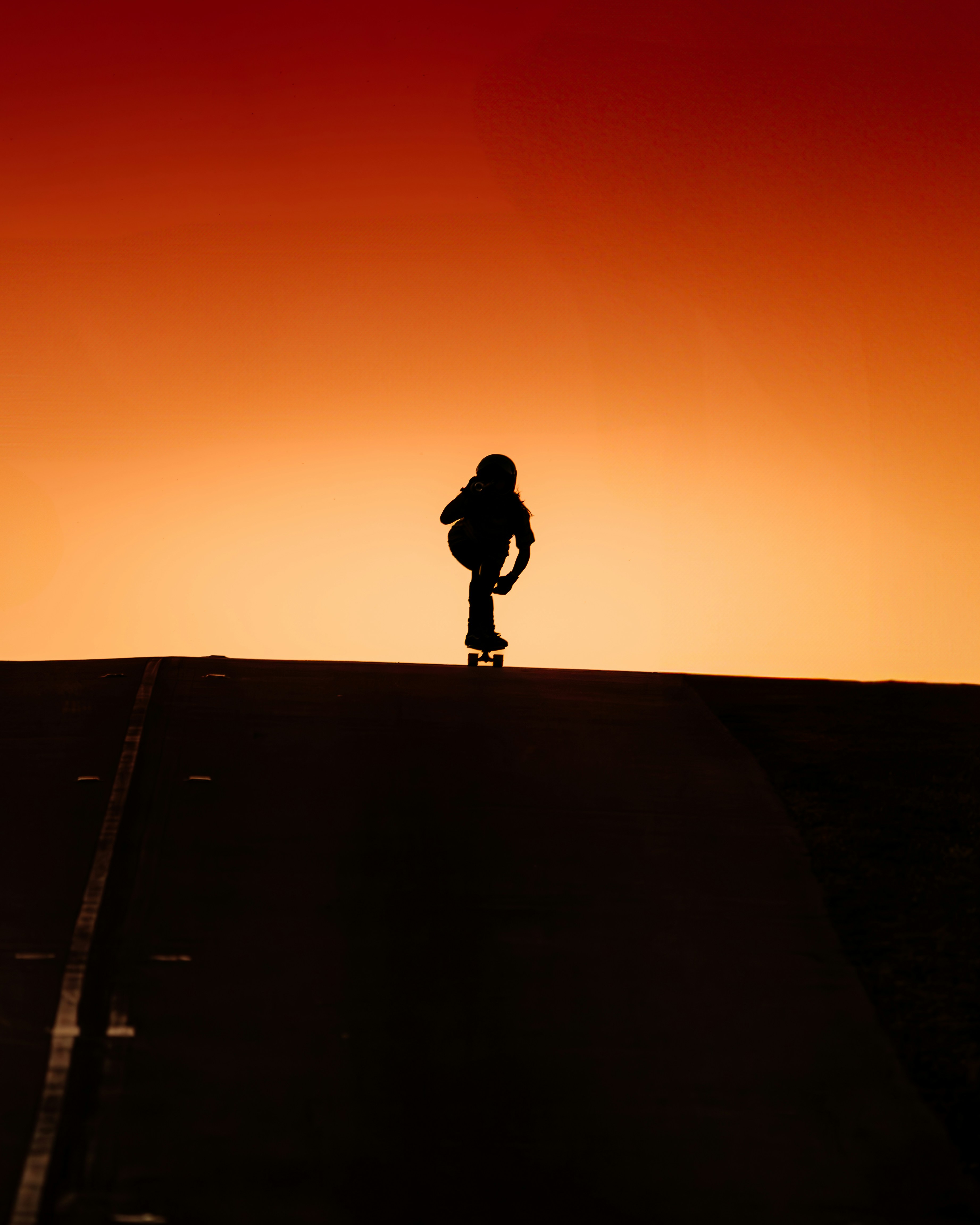 Silhouette of a skateboarder gliding along a path against a vibrant orange gradient sky.