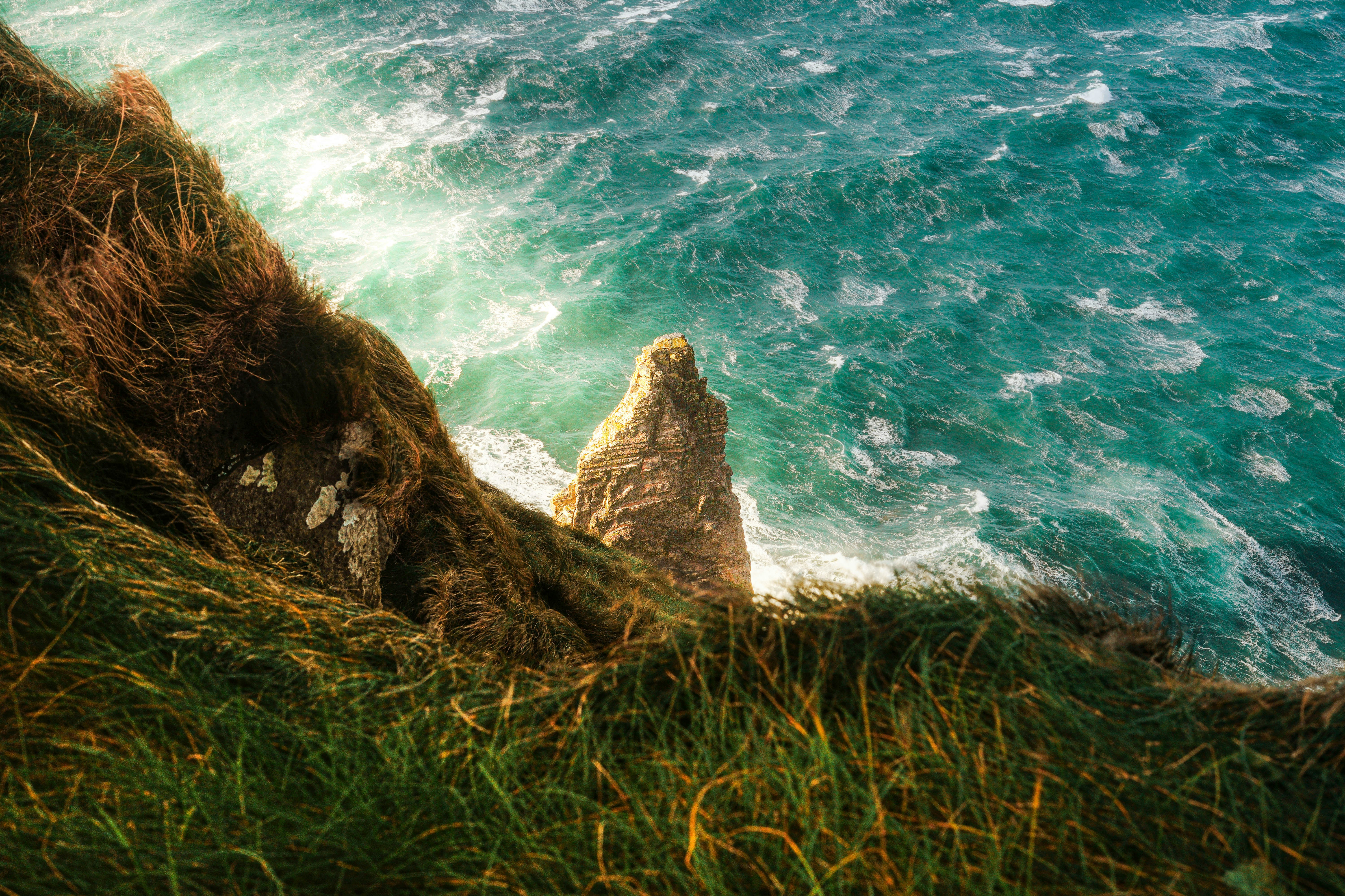 Rugged cliffside overlooking a turbulent ocean with vibrant turquoise waves.