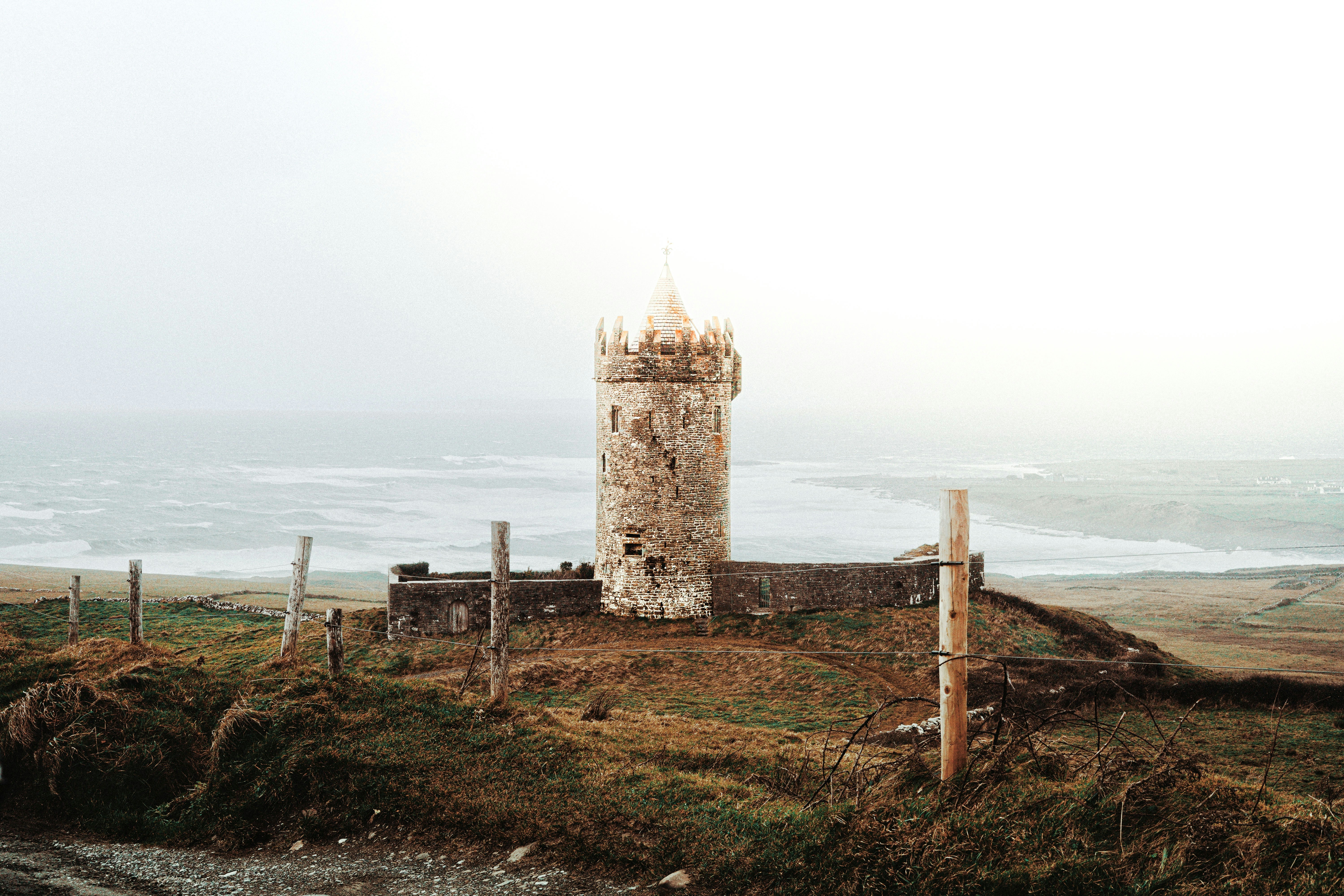 Stone tower overlooking a misty shoreline with rolling green hills.