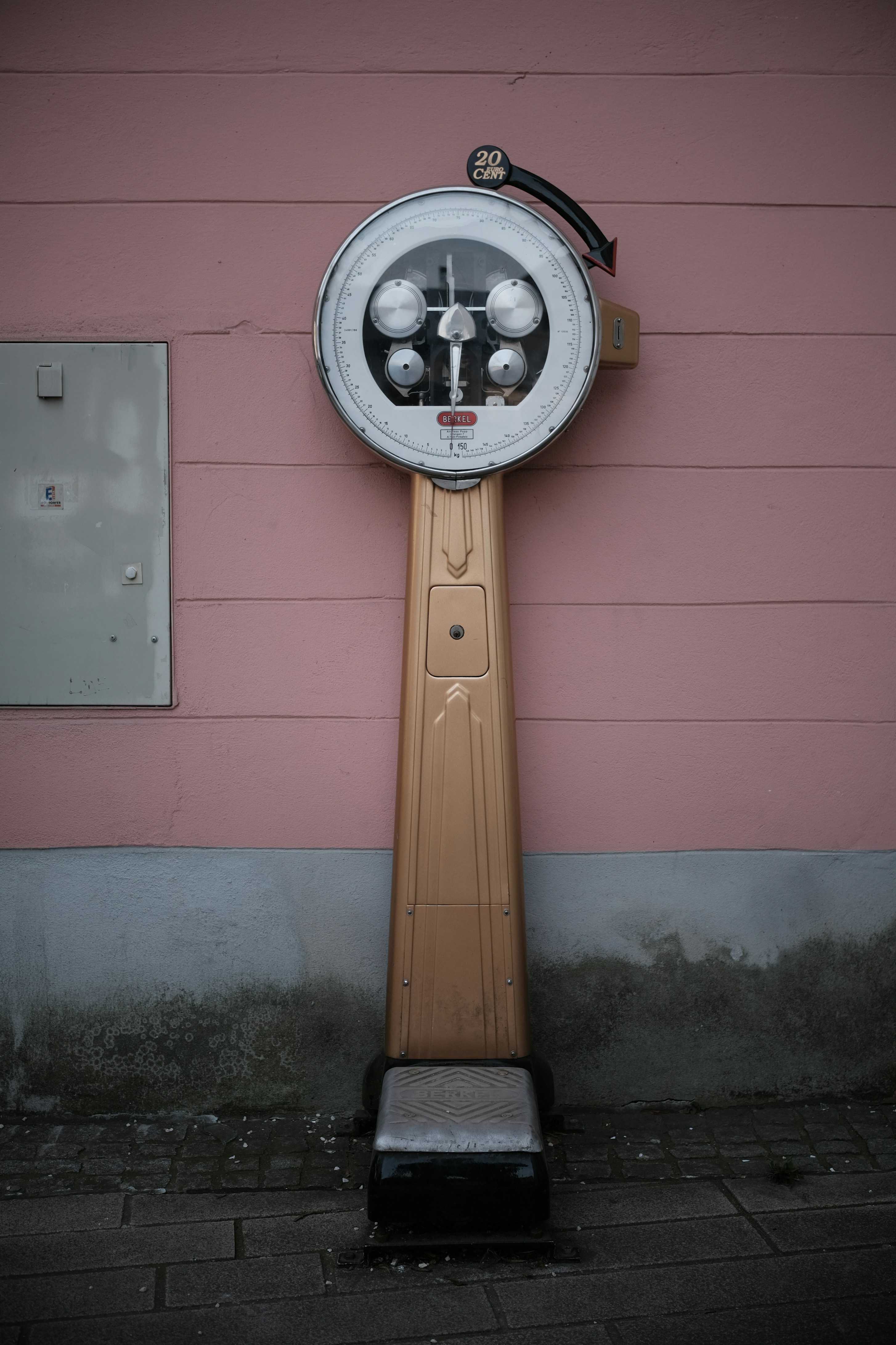 Retro weighing scale mounted against a soft pink wall, showcasing its vintage design and charm.