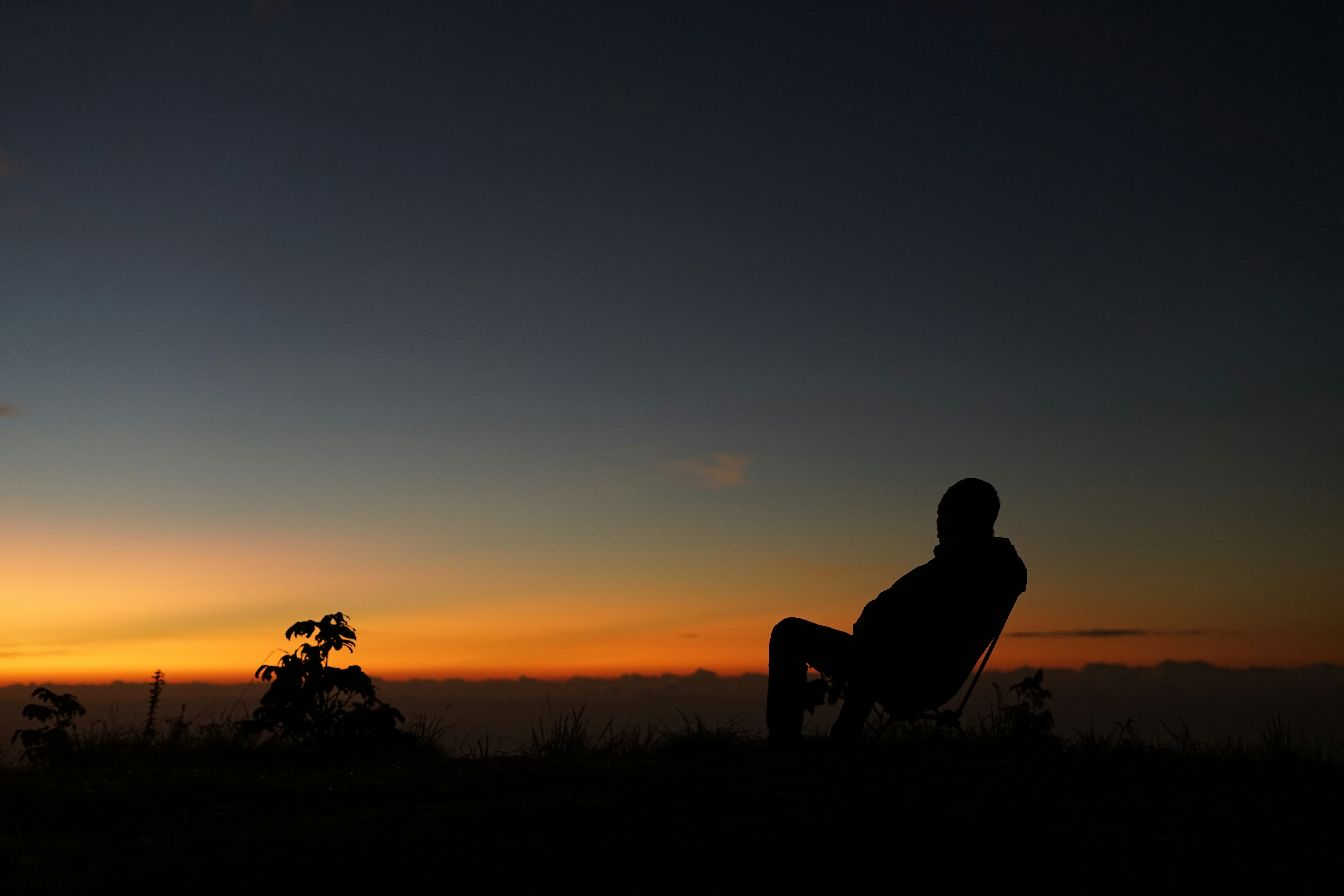 Silhouette of a person sitting against a vibrant sunrise sky on Mount Rinjani's southern route.