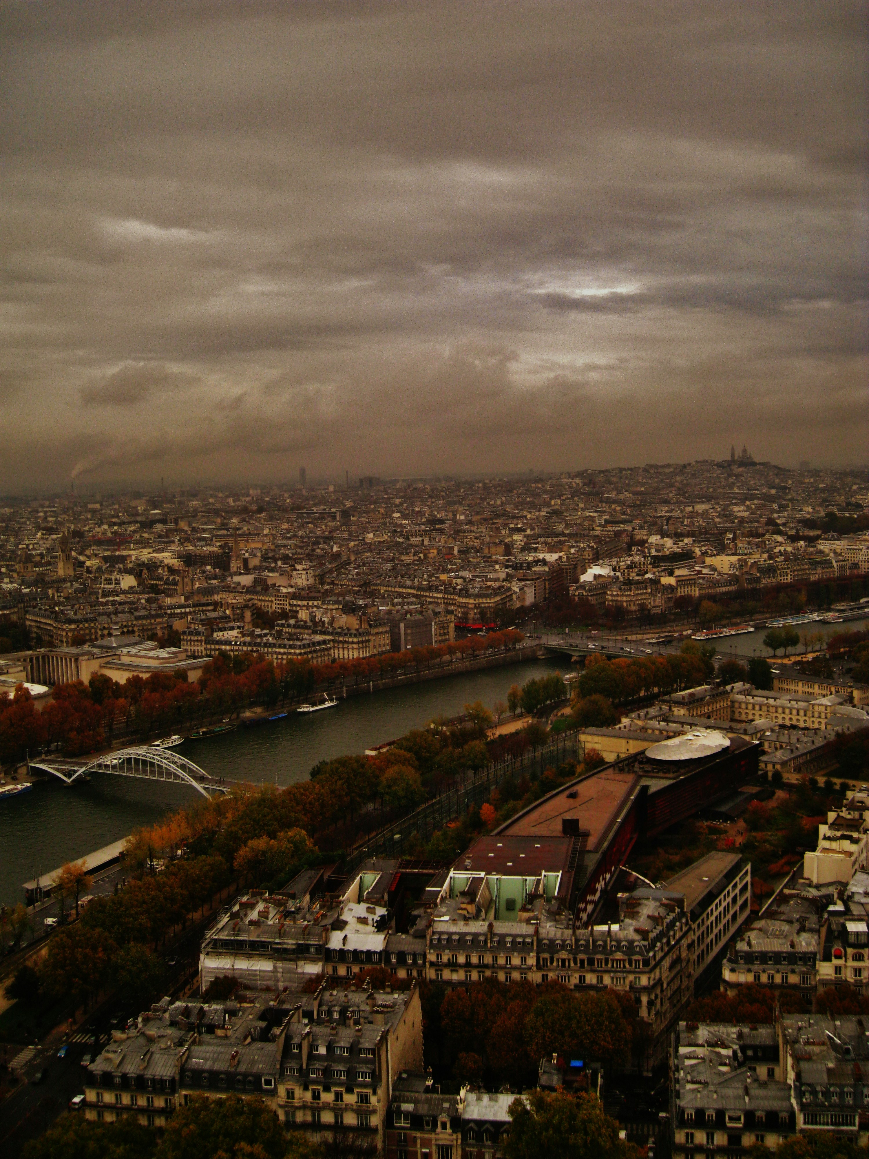 Aerial cityscape along a winding river at dusk, with a white arched bridge and rows of autumn-colored rooftops.