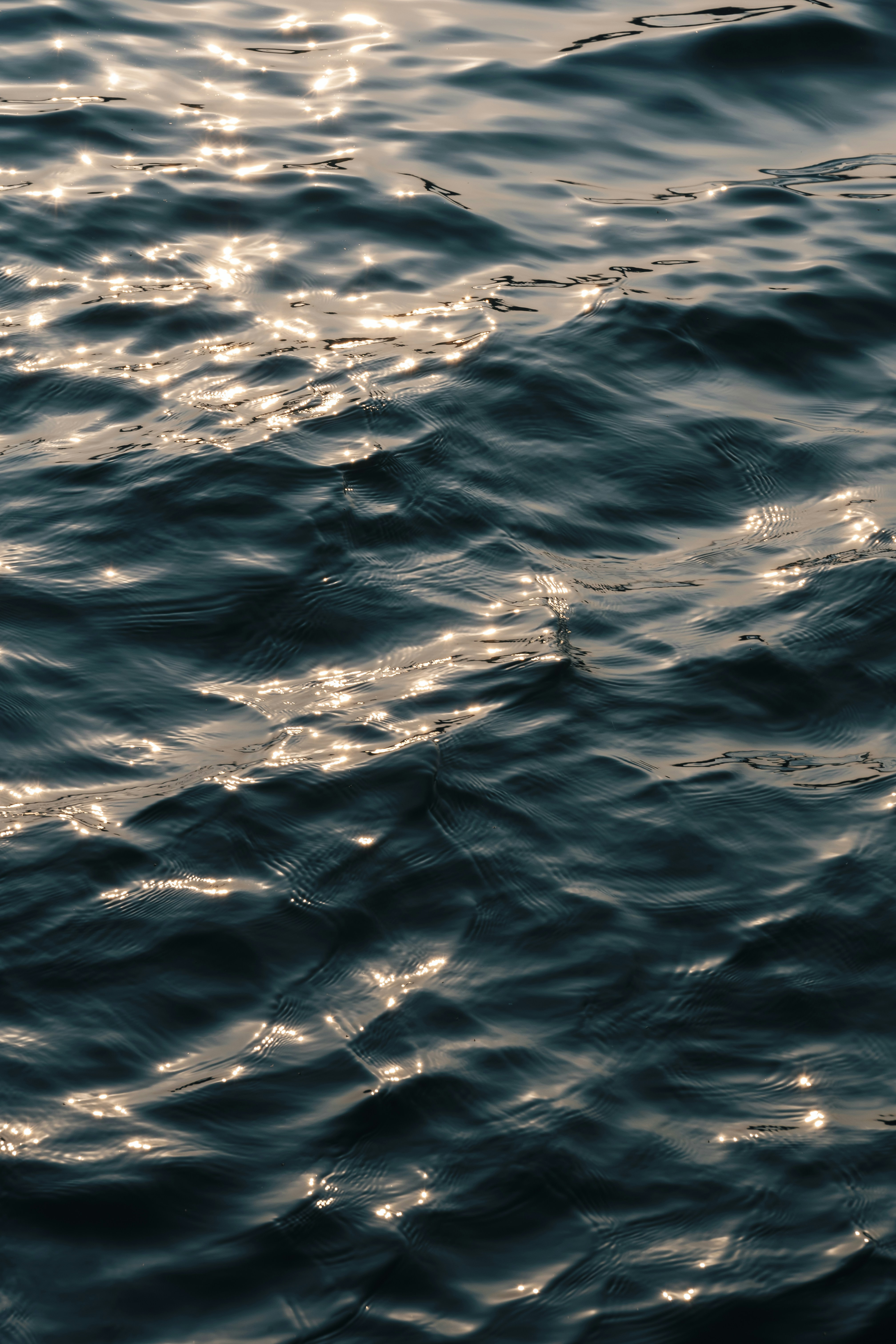 Sun-dappled sea surface with gentle waves and bright reflections creating a textured, abstract pattern.