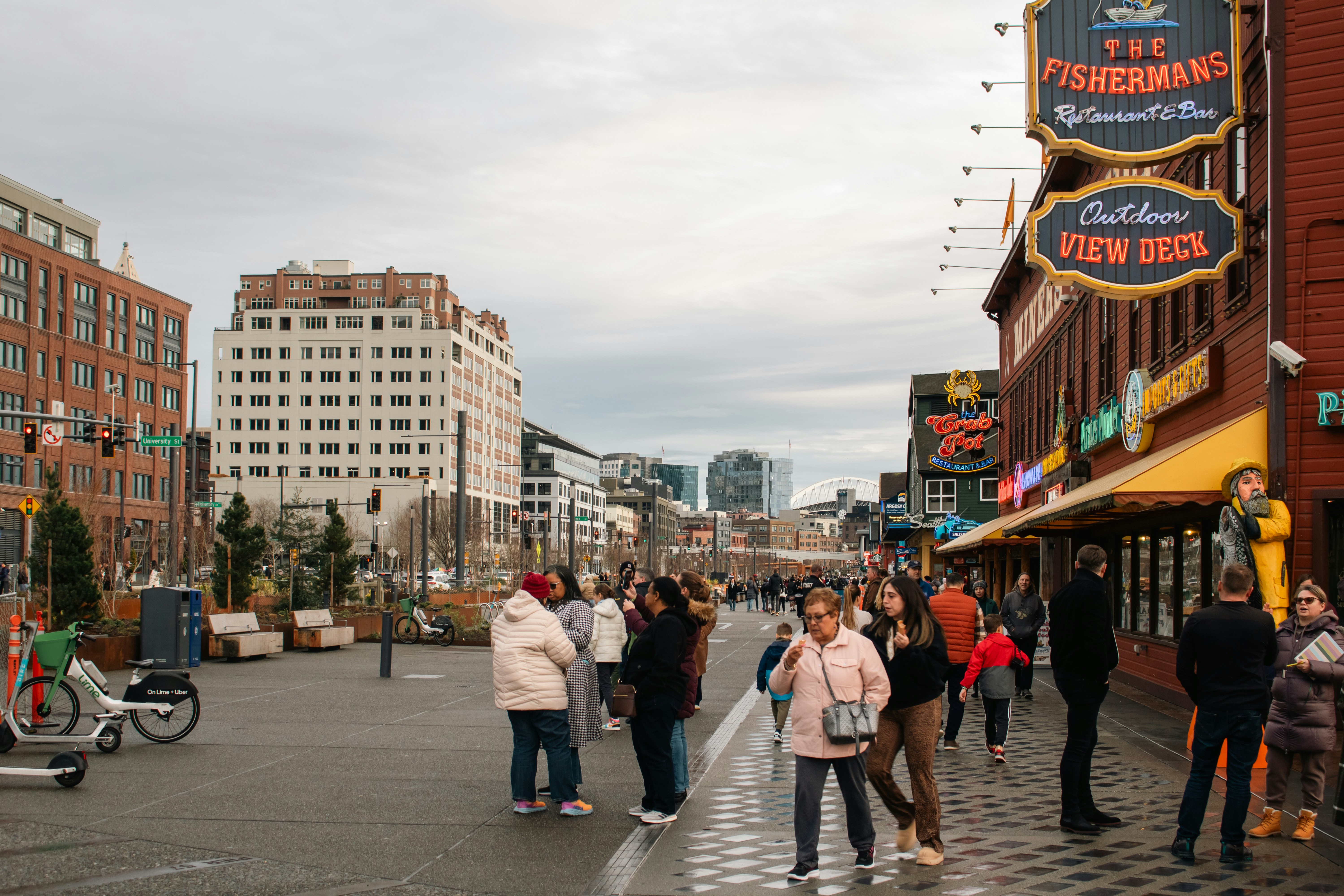 People stroll past shops and eateries along a bustling waterfront in Seattle.