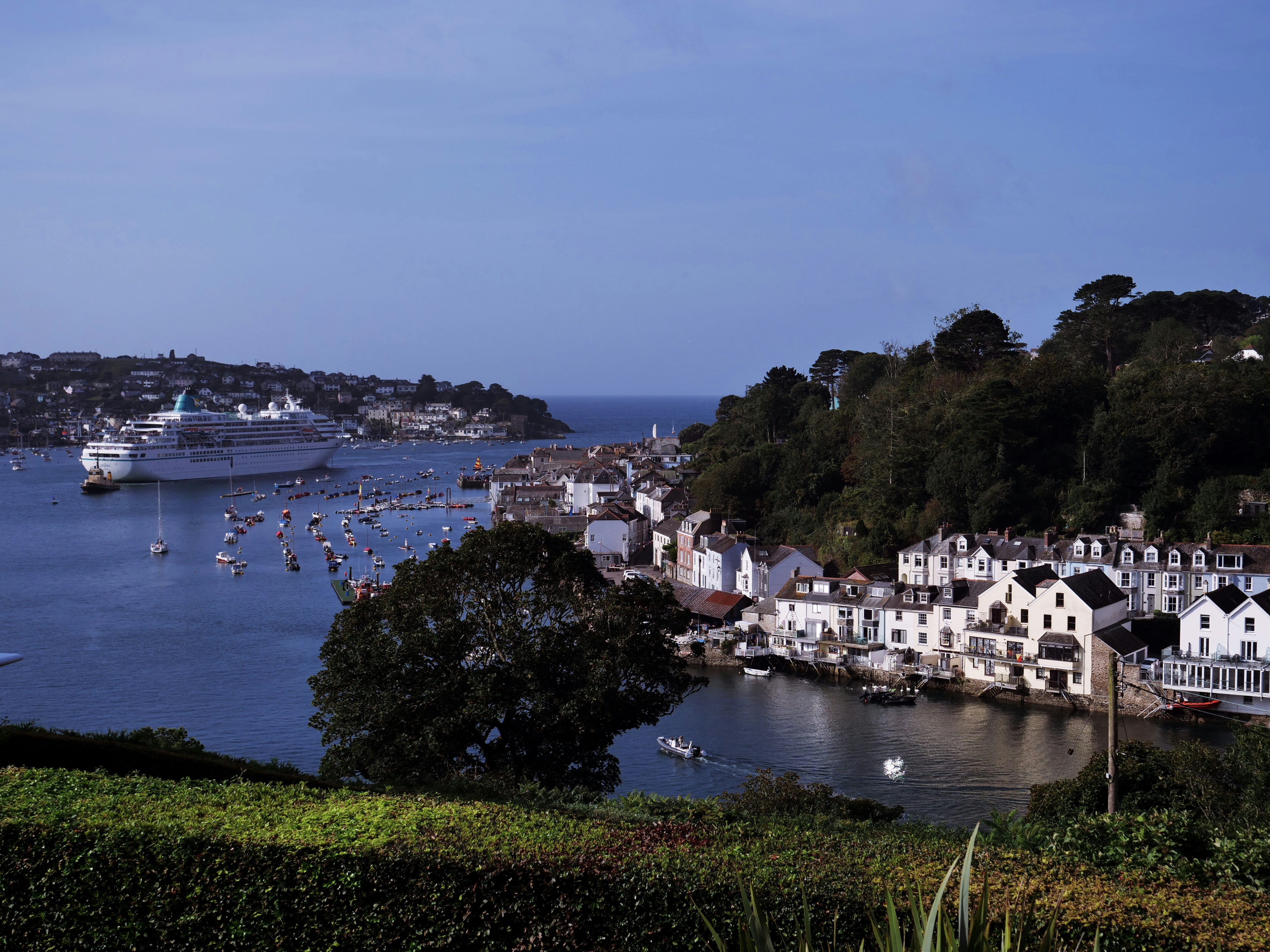 Cruise ship departing a picturesque harbor town under a clear blue sky.