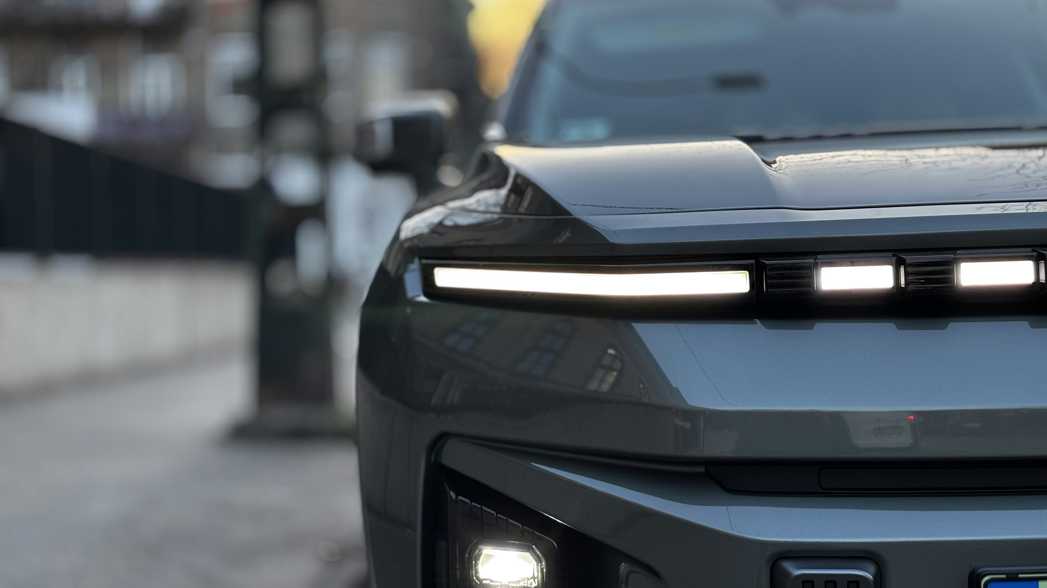 Sleek front view of a futuristic car with LED headlights and a streamlined grille, parked on a city street at dusk.