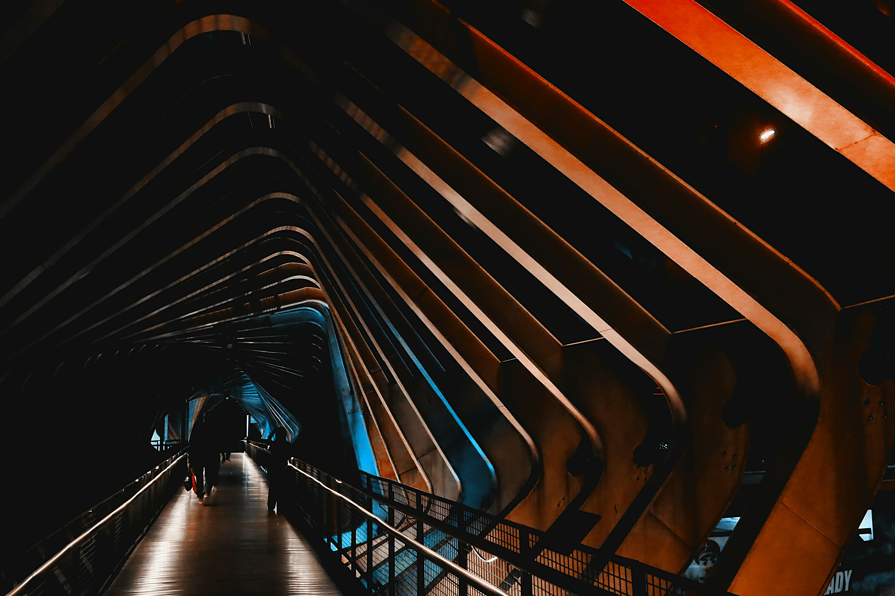 Silhouetted figures walk through a futuristic tunnel with glowing beams and intricate architectural patterns.