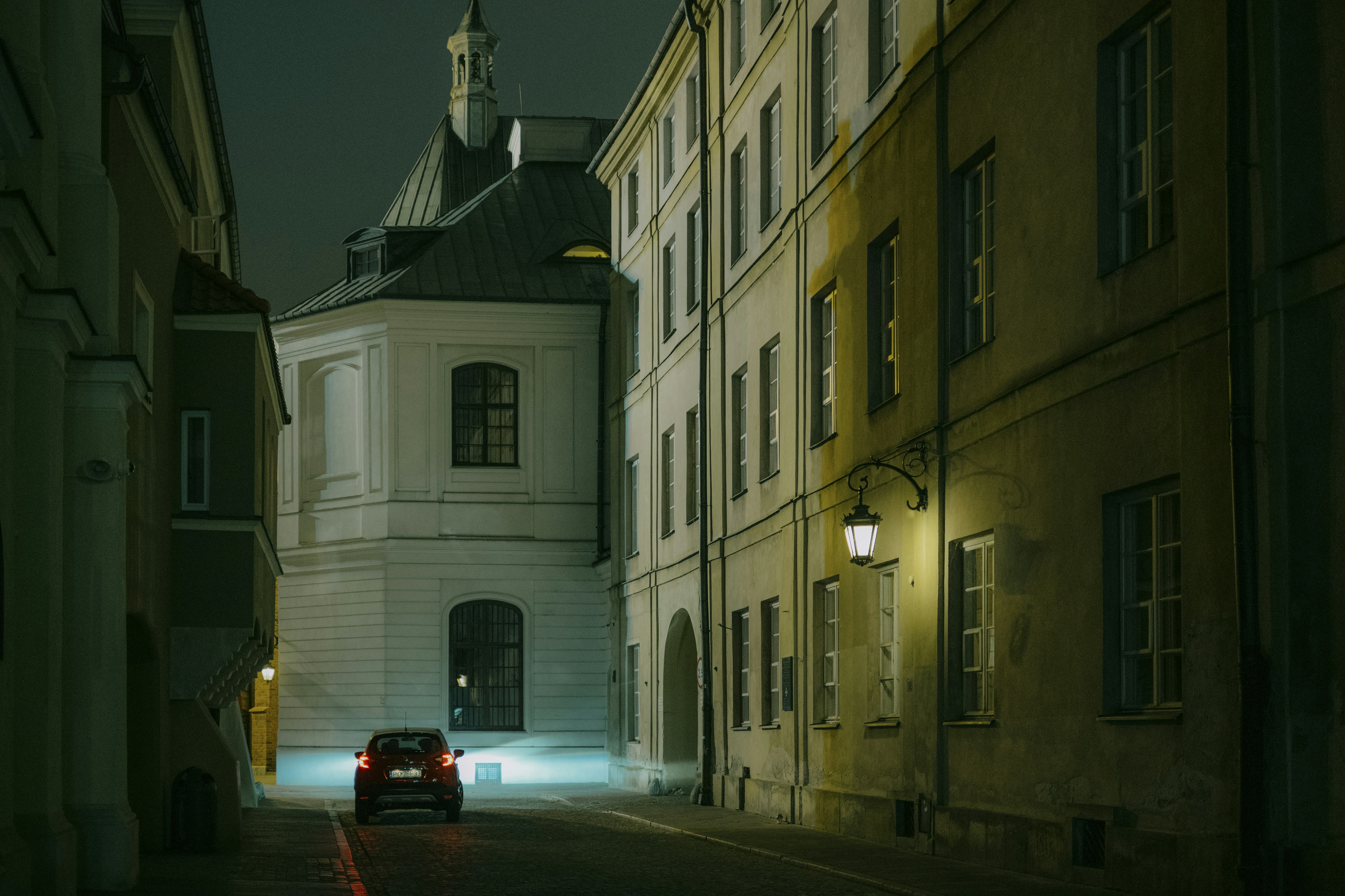 A car drives down a dimly lit city street at night. photo – Free Green ...