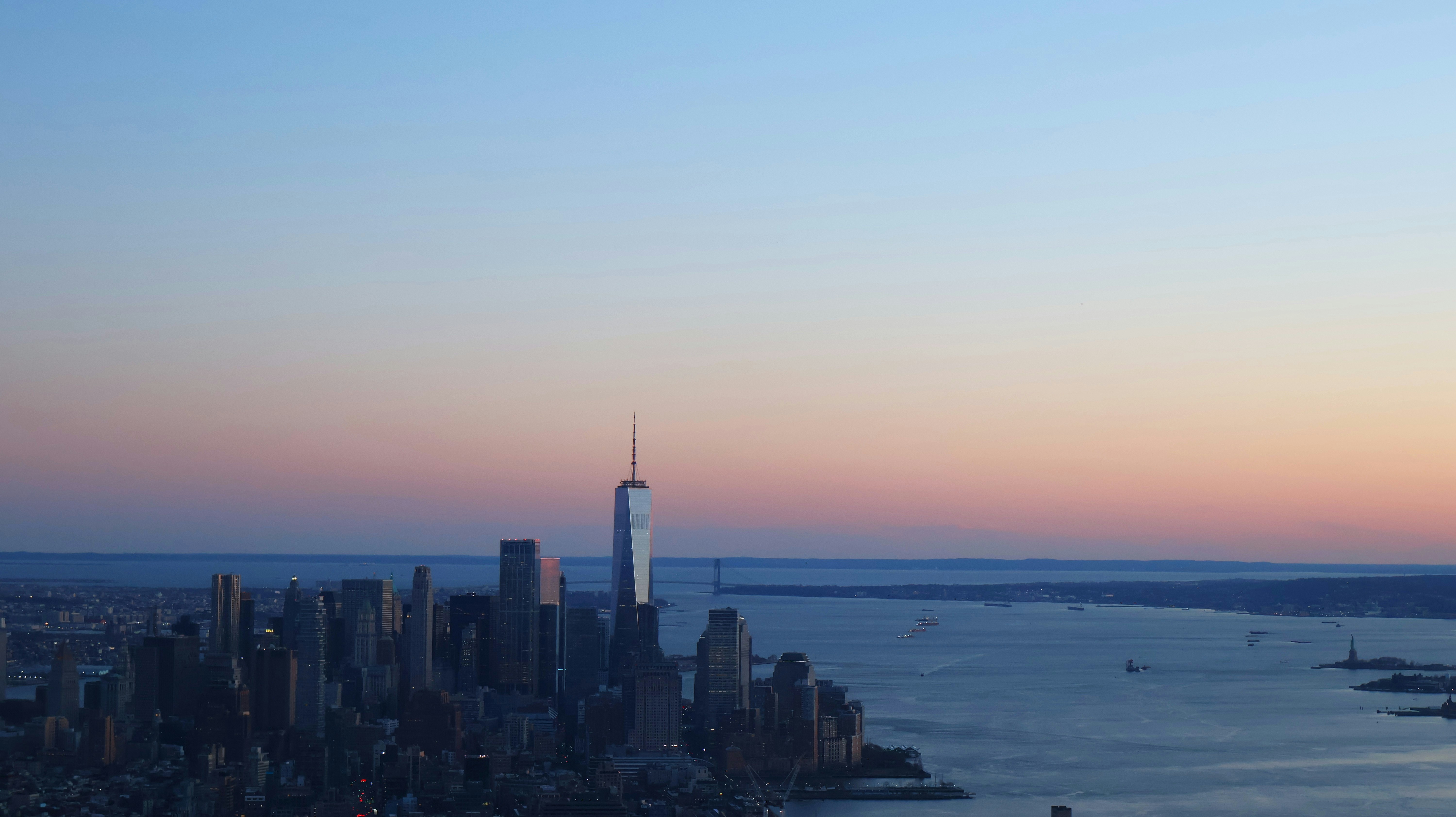 New York City skyline silhouetted against a gradient sunset sky, with the river reflecting pastel hues.