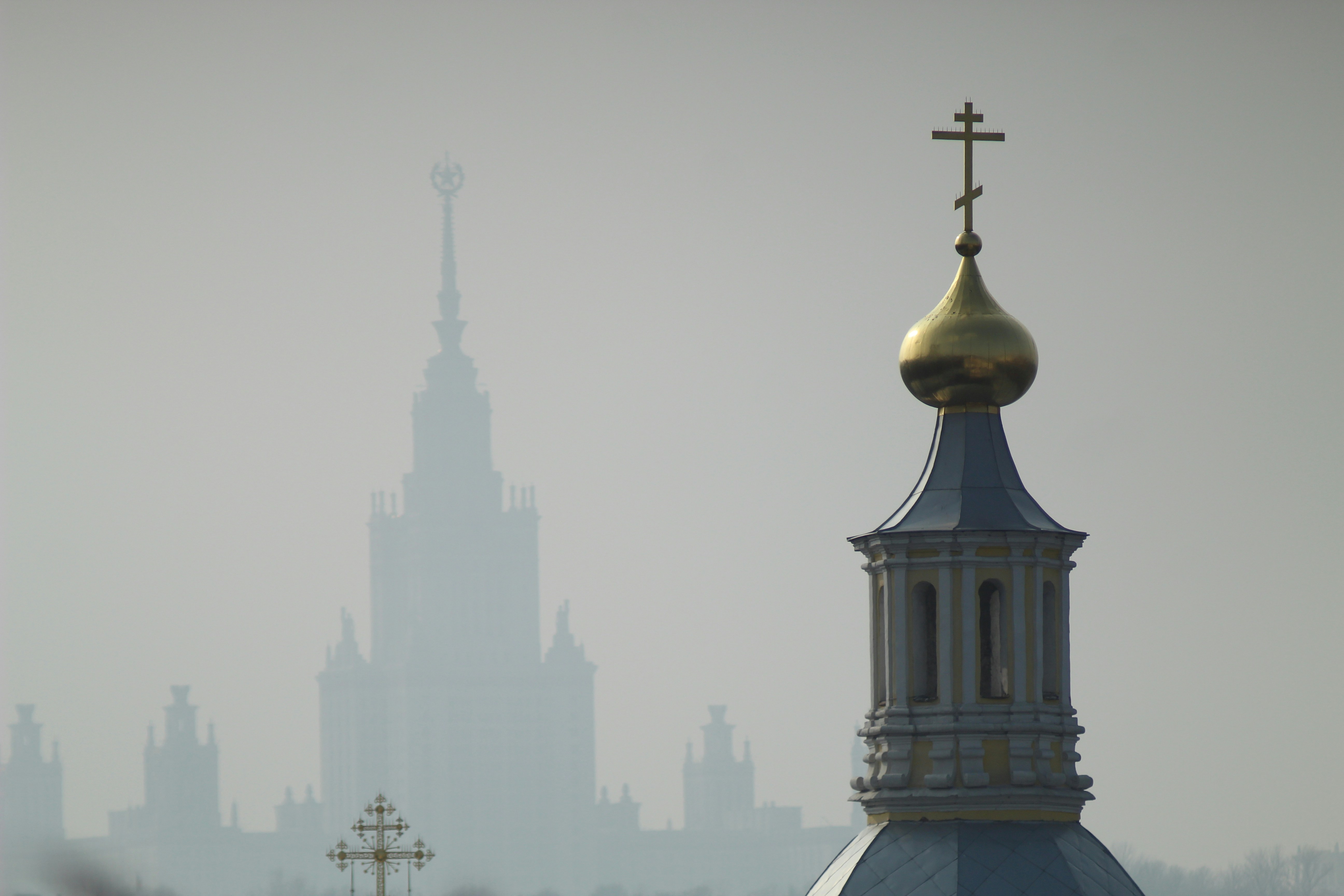Church spire in focus with a distant city building shrouded in fog.