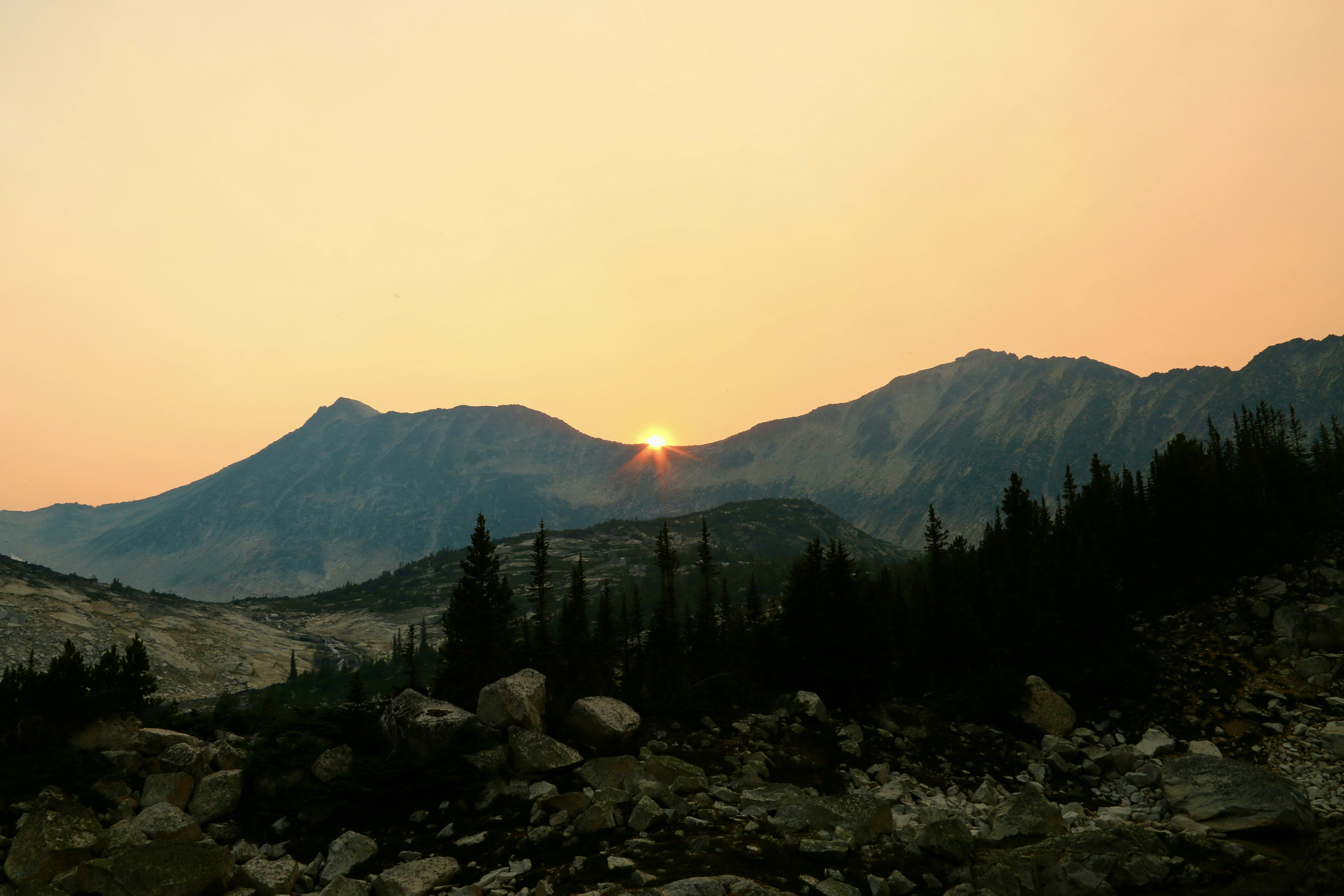Dawn Breaks Over a Rugged Ridge: Sunlight Between Peaks and a Rocky Foreground