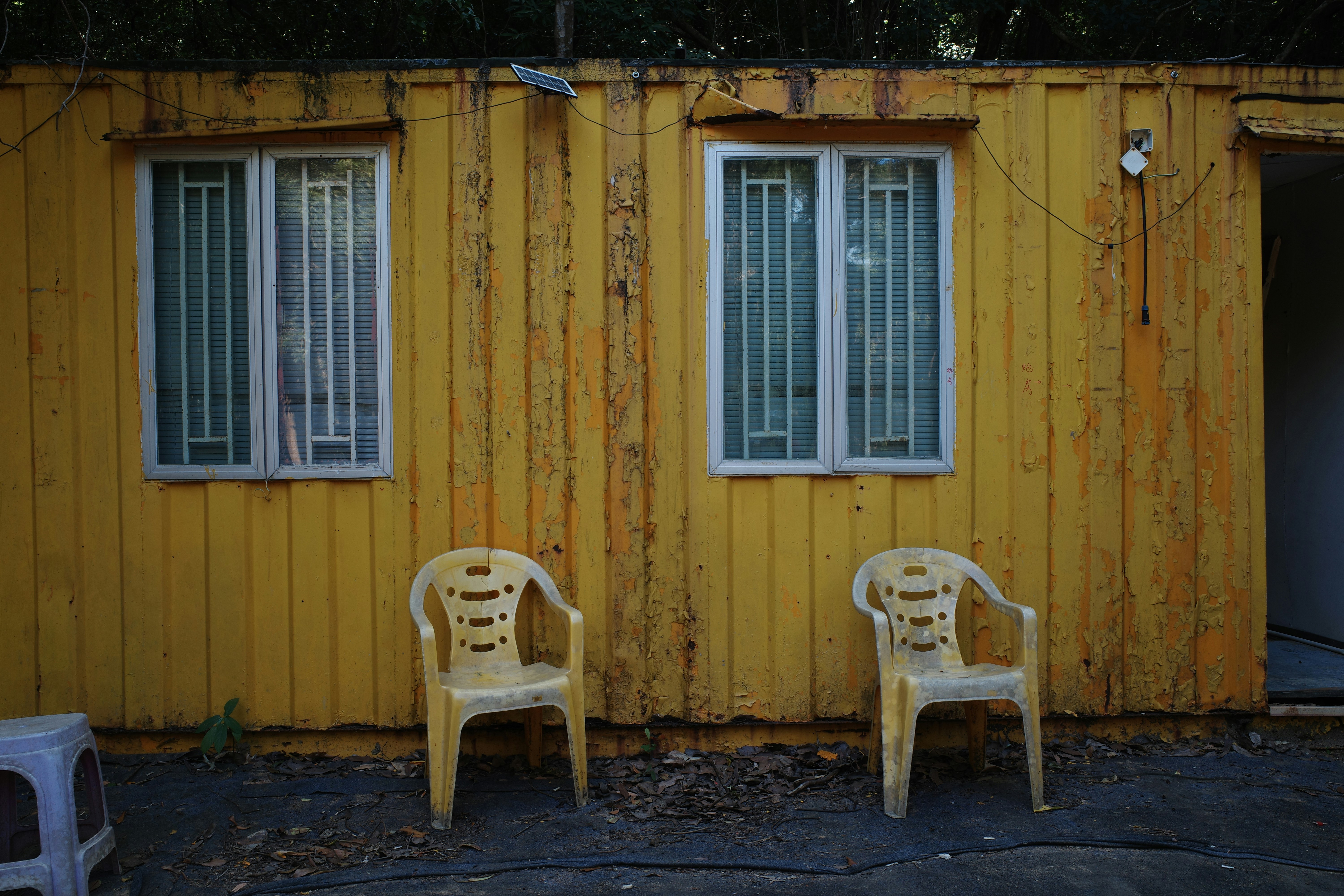 Peeling yellow paint on a building with two empty plastic chairs outside.