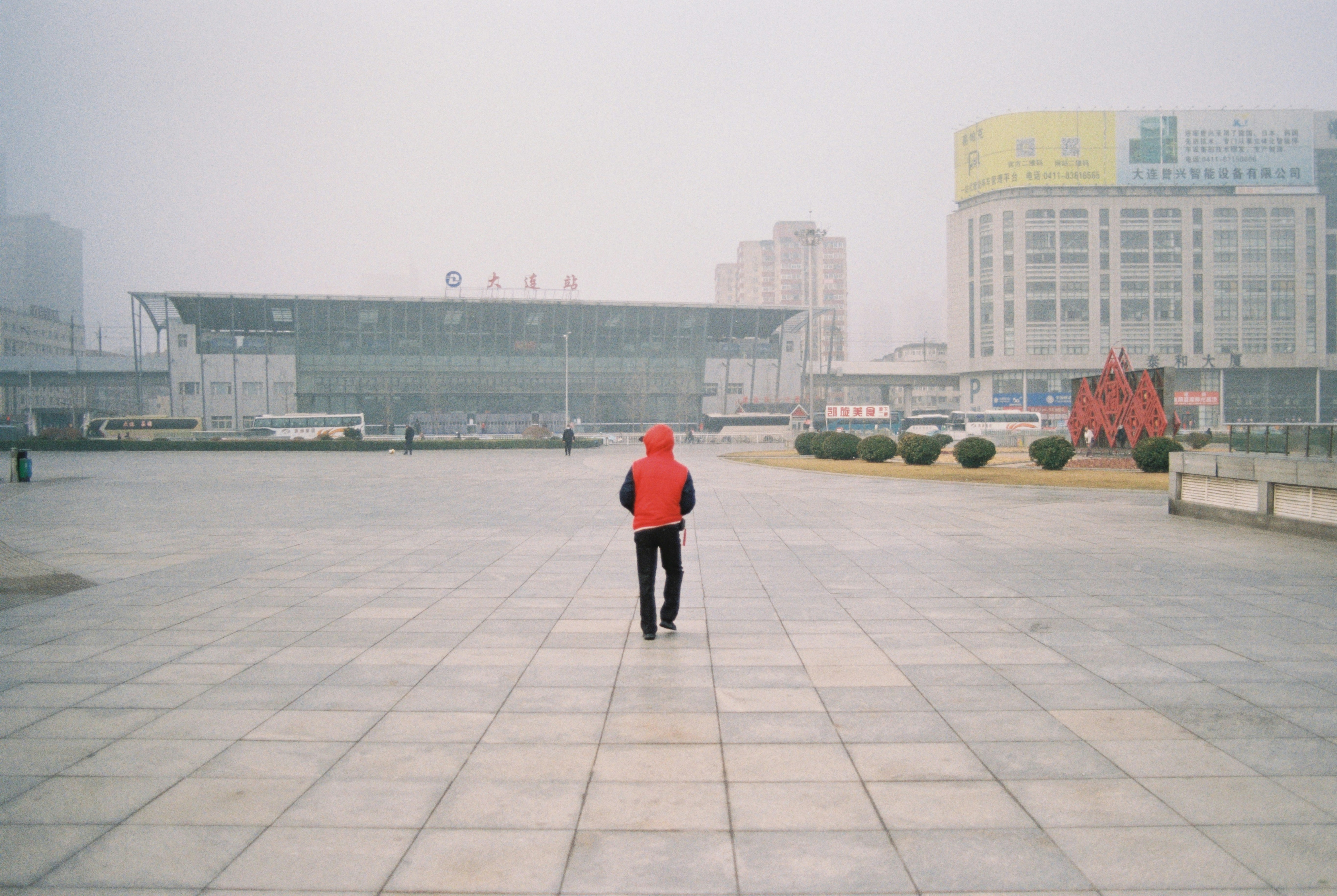 Person in a red jacket walks across a foggy plaza towards a modern building.